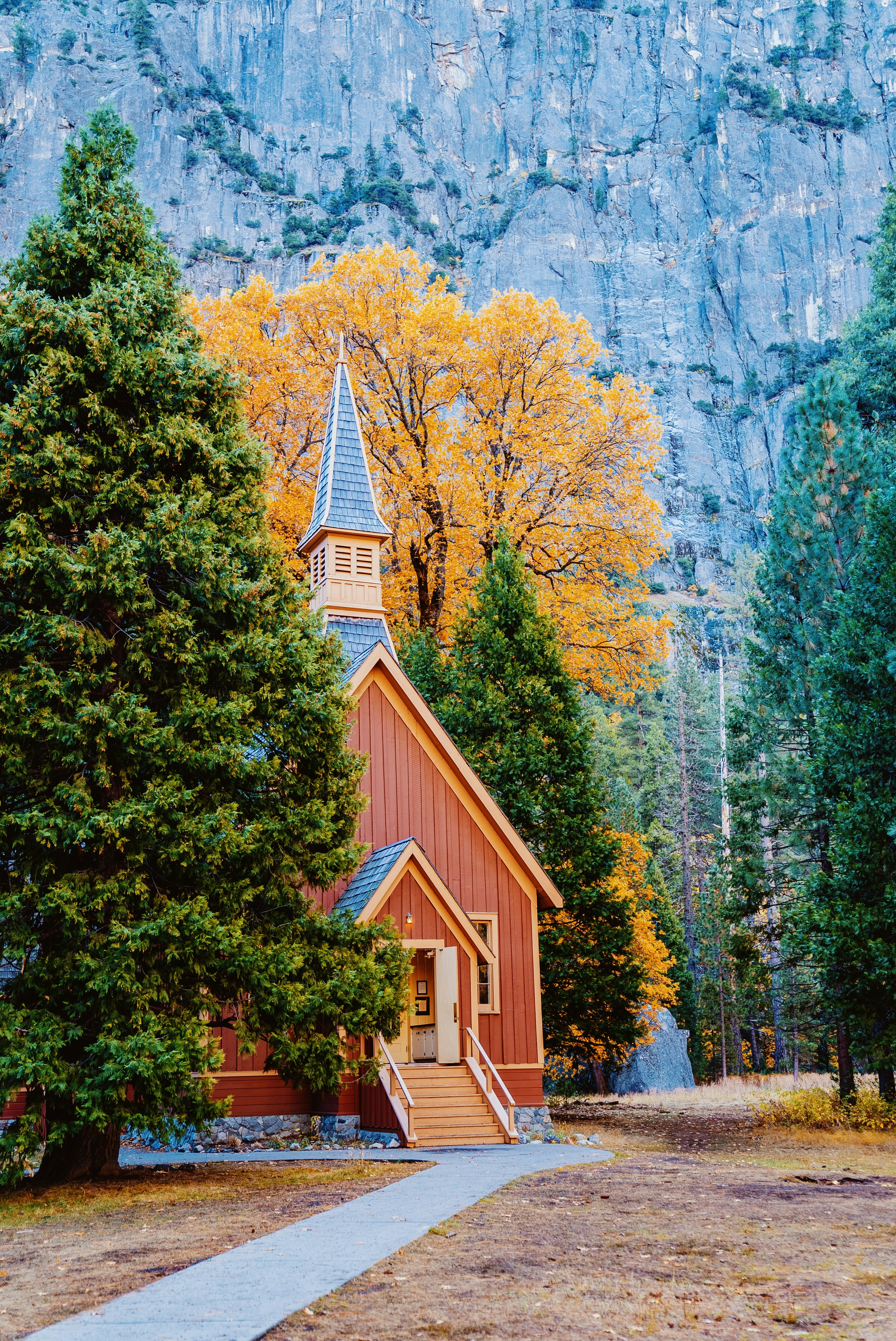 Charming wooden chapel surrounded by vibrant autumn foliage and towering trees, set against a rocky backdrop. 