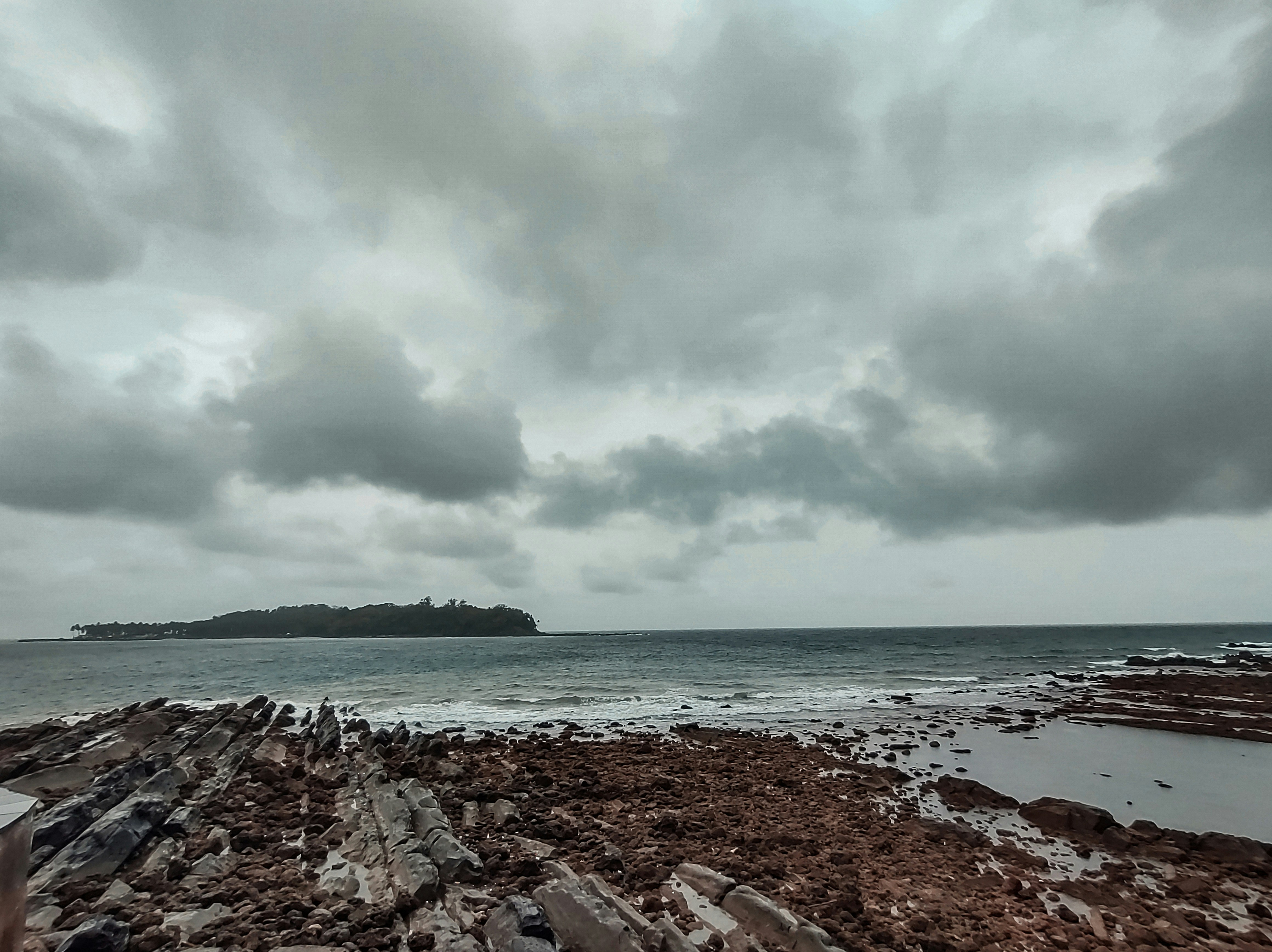 Rugged coastal rocks stretch towards a distant island under a moody sky, evoking a sense of tranquility and solitude.