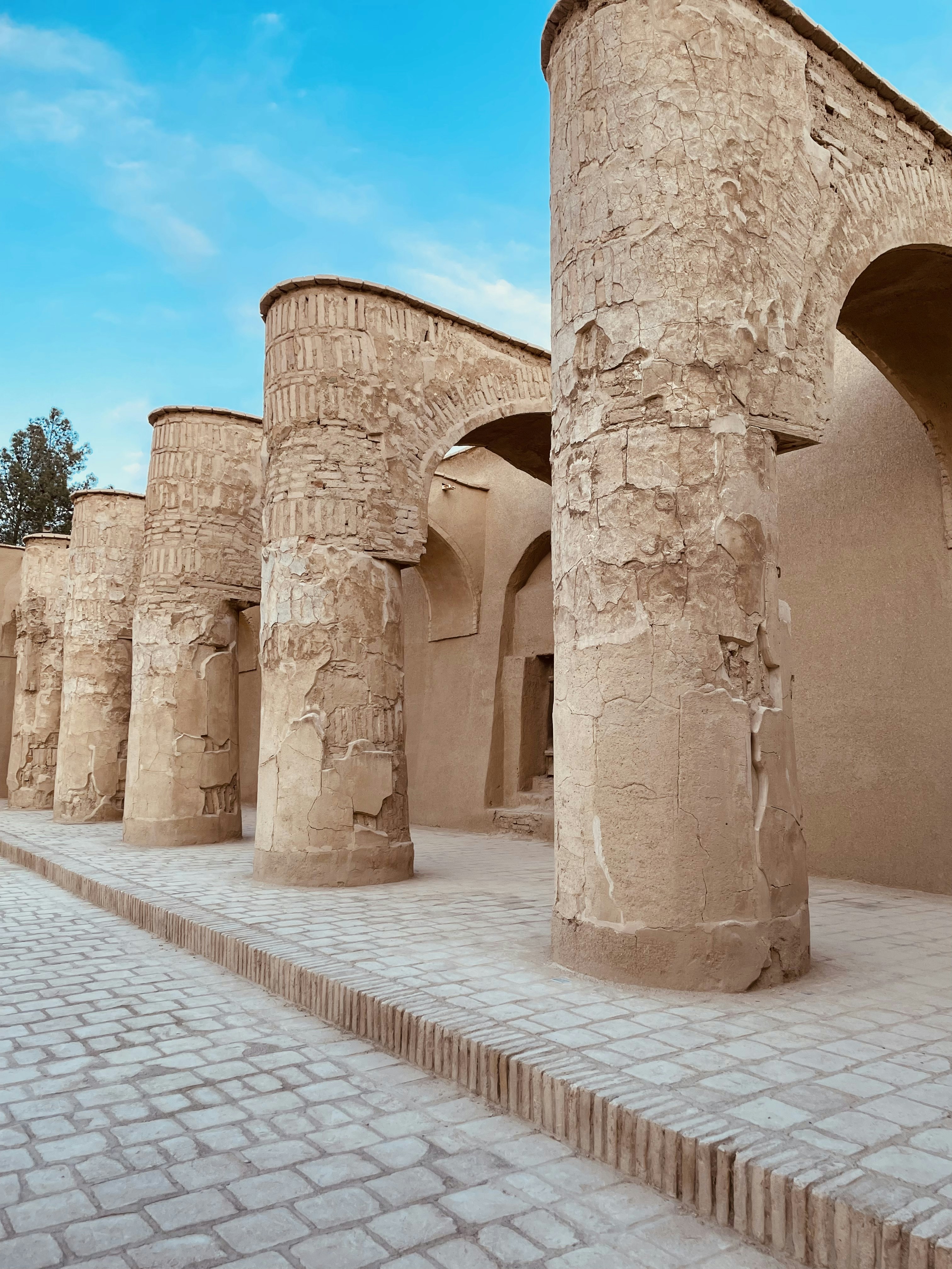 Row of weathered stone pillars in an old architectural site against a clear blue sky.