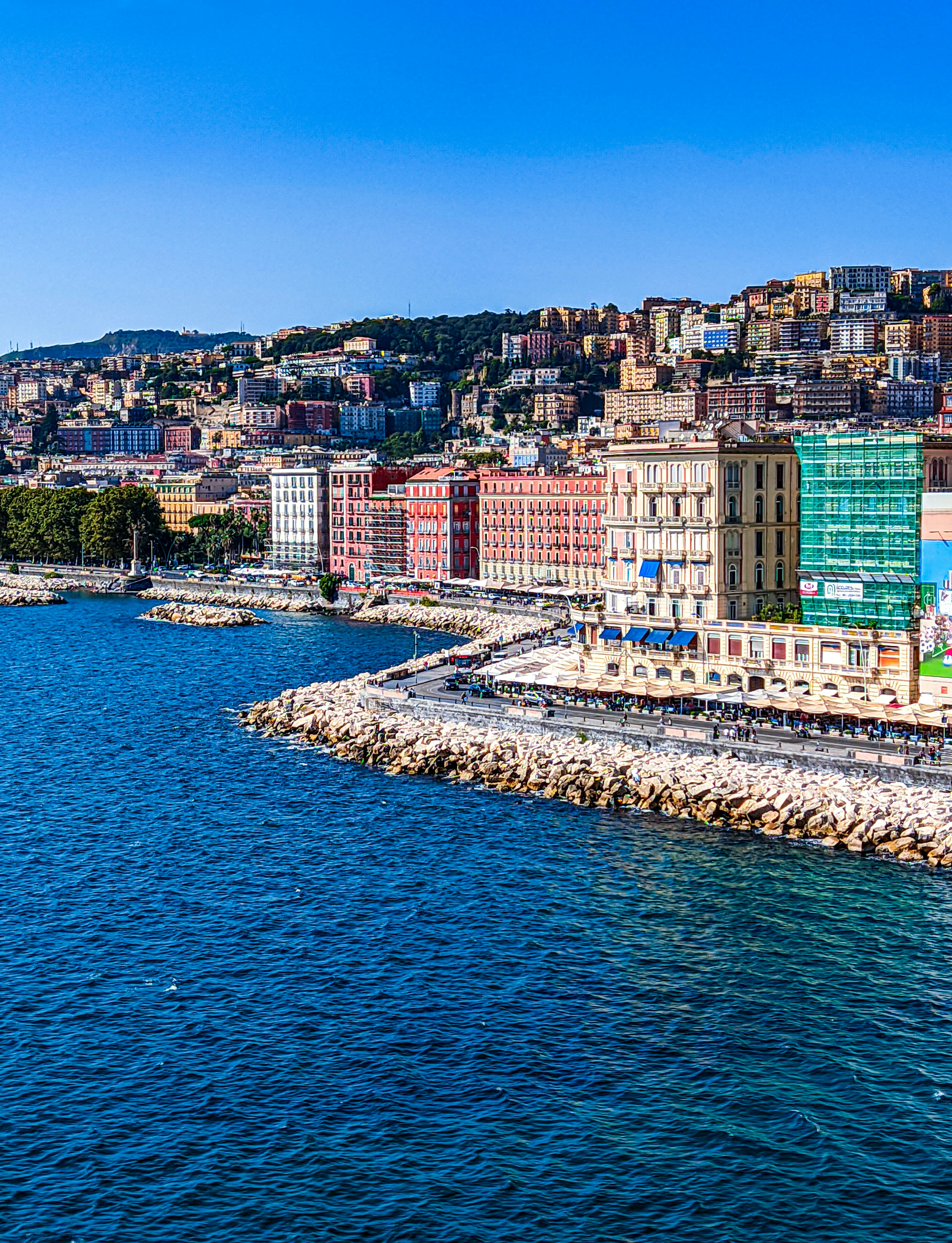 Colorful waterfront photograph capturing pastel façades along a rocky quay, with deep blue sea and a clear sky.
