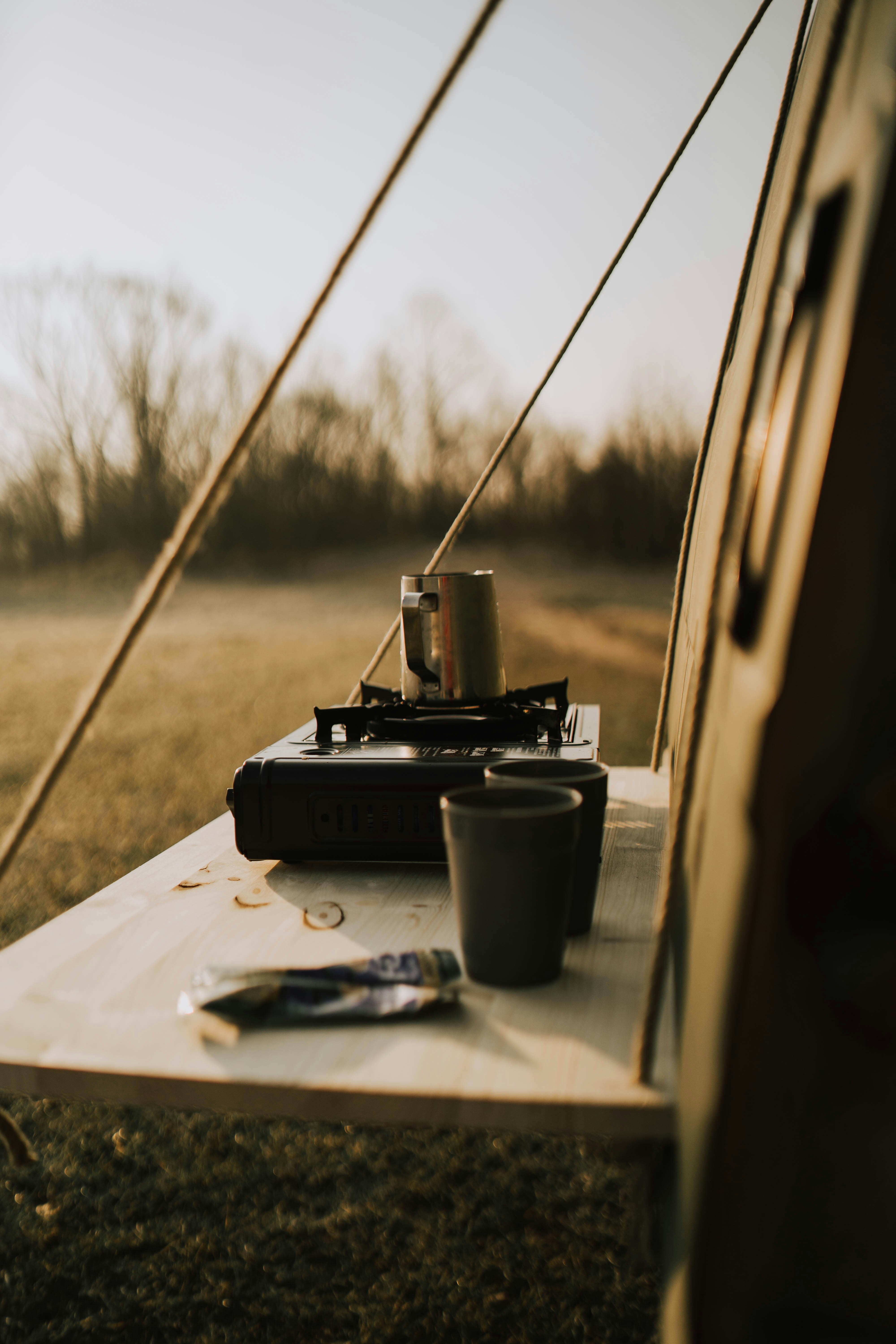 Camping stove with a kettle and a cup on a wooden table, set against a misty morning backdrop. The scene evokes a sense of tranquility and adventure.
