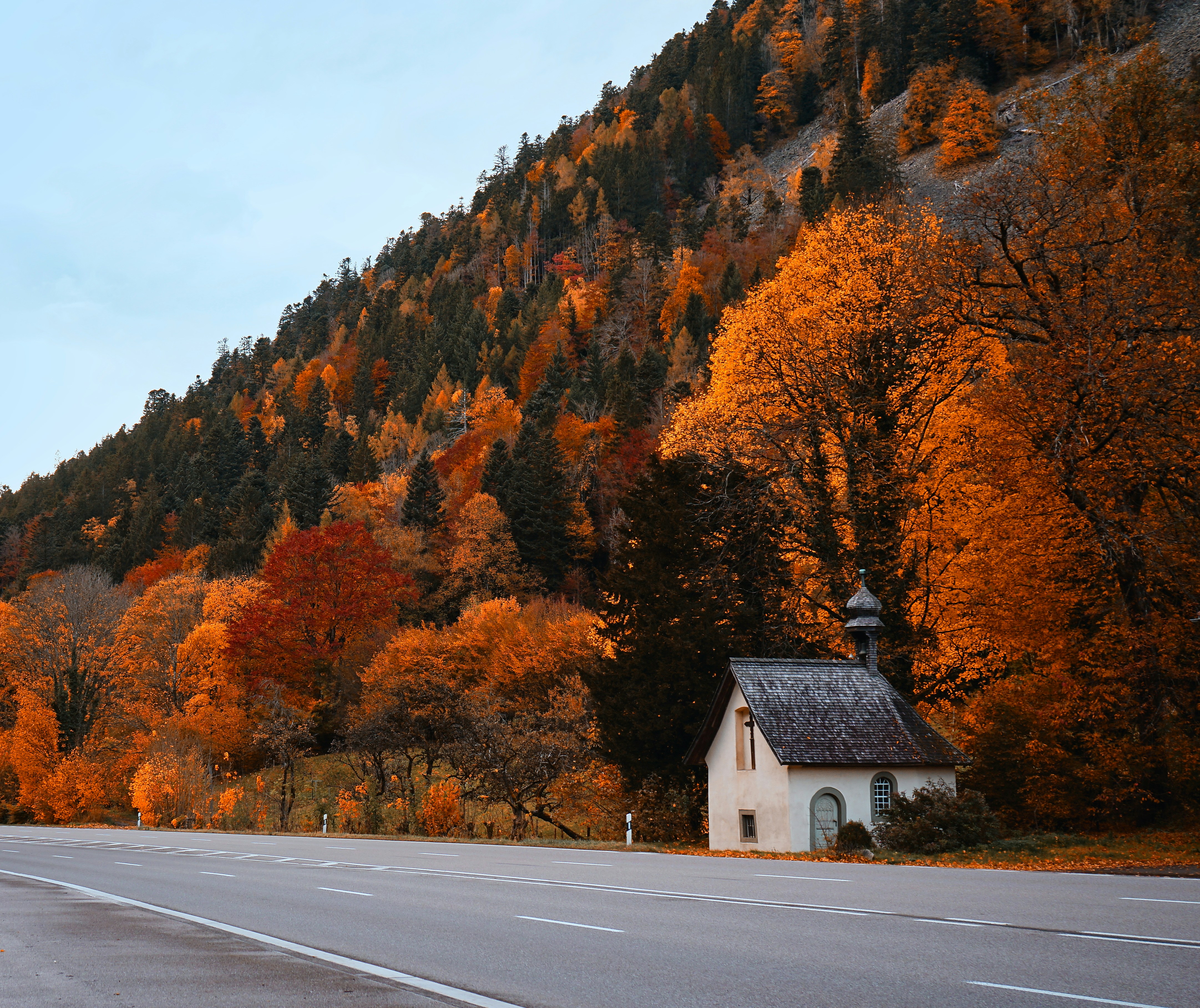 Small chapel nestled among vibrant autumn trees near a quiet road.