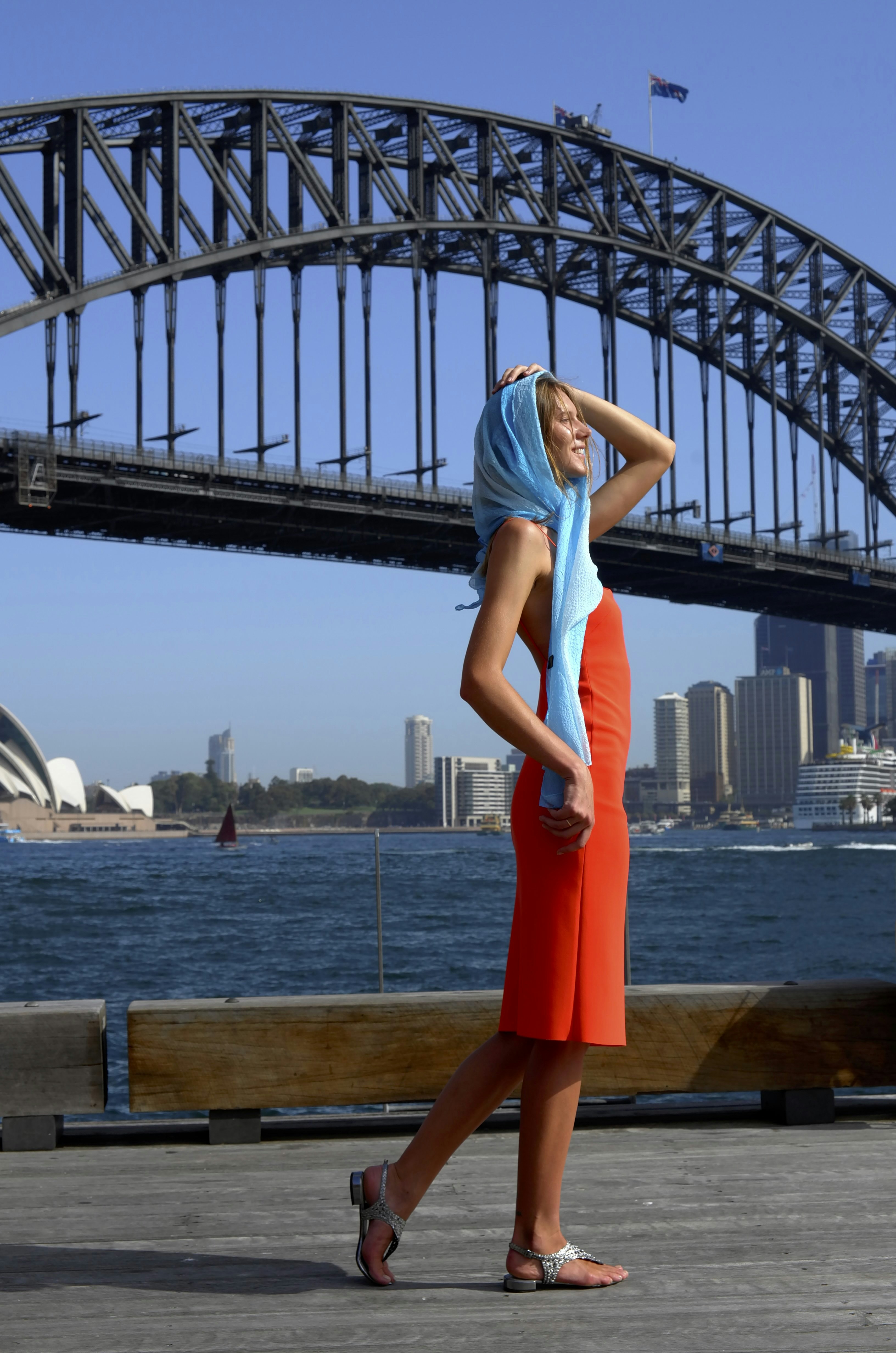 Scarlet silhouette under the bridge: a sunlit pose by Sydney Harbor