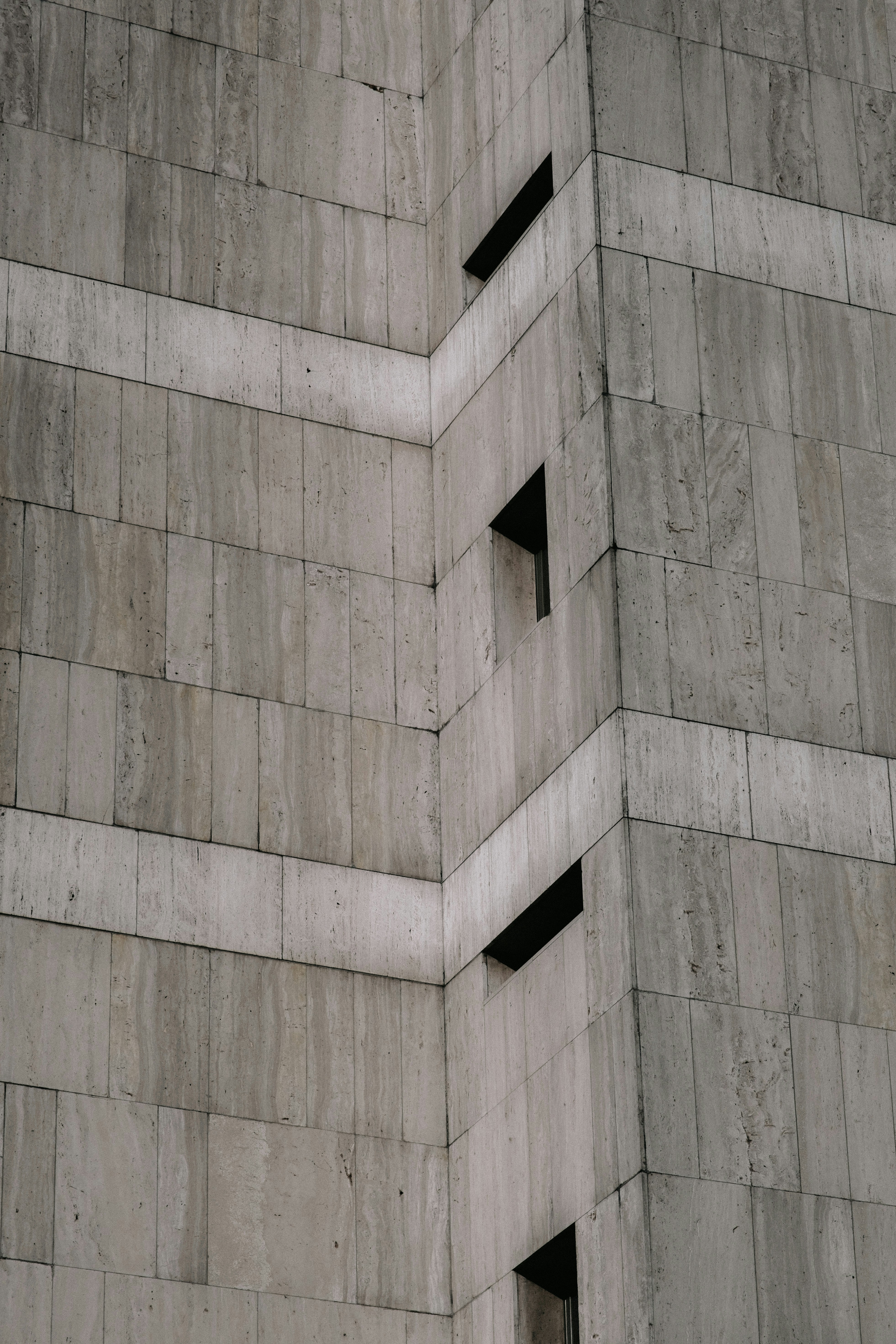 Close-up of a modern building's textured concrete facade, highlighting the interplay of light and shadow on angular surfaces.