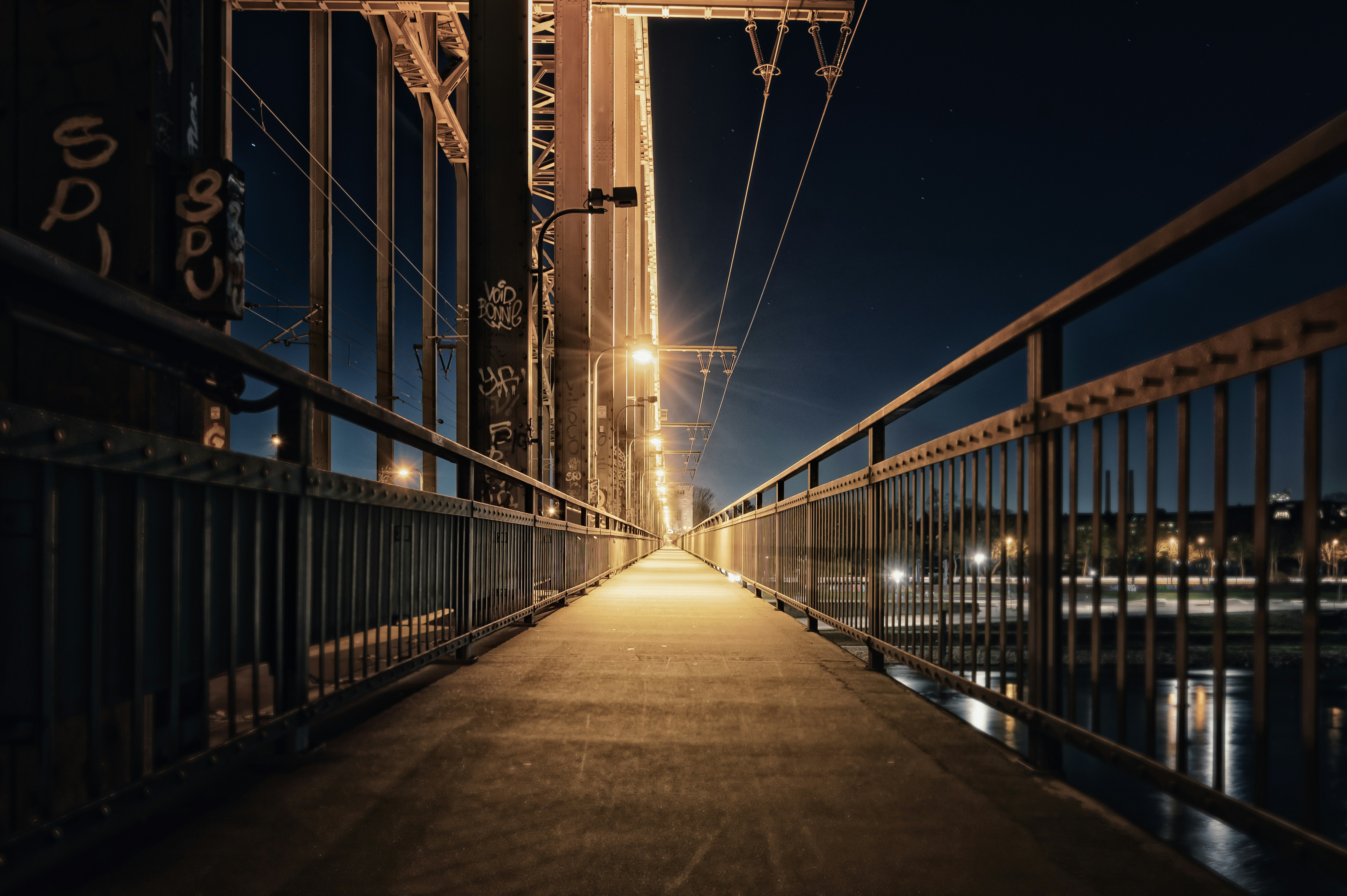 Illuminated bridge walkway under a night sky with city lights reflecting on the water.