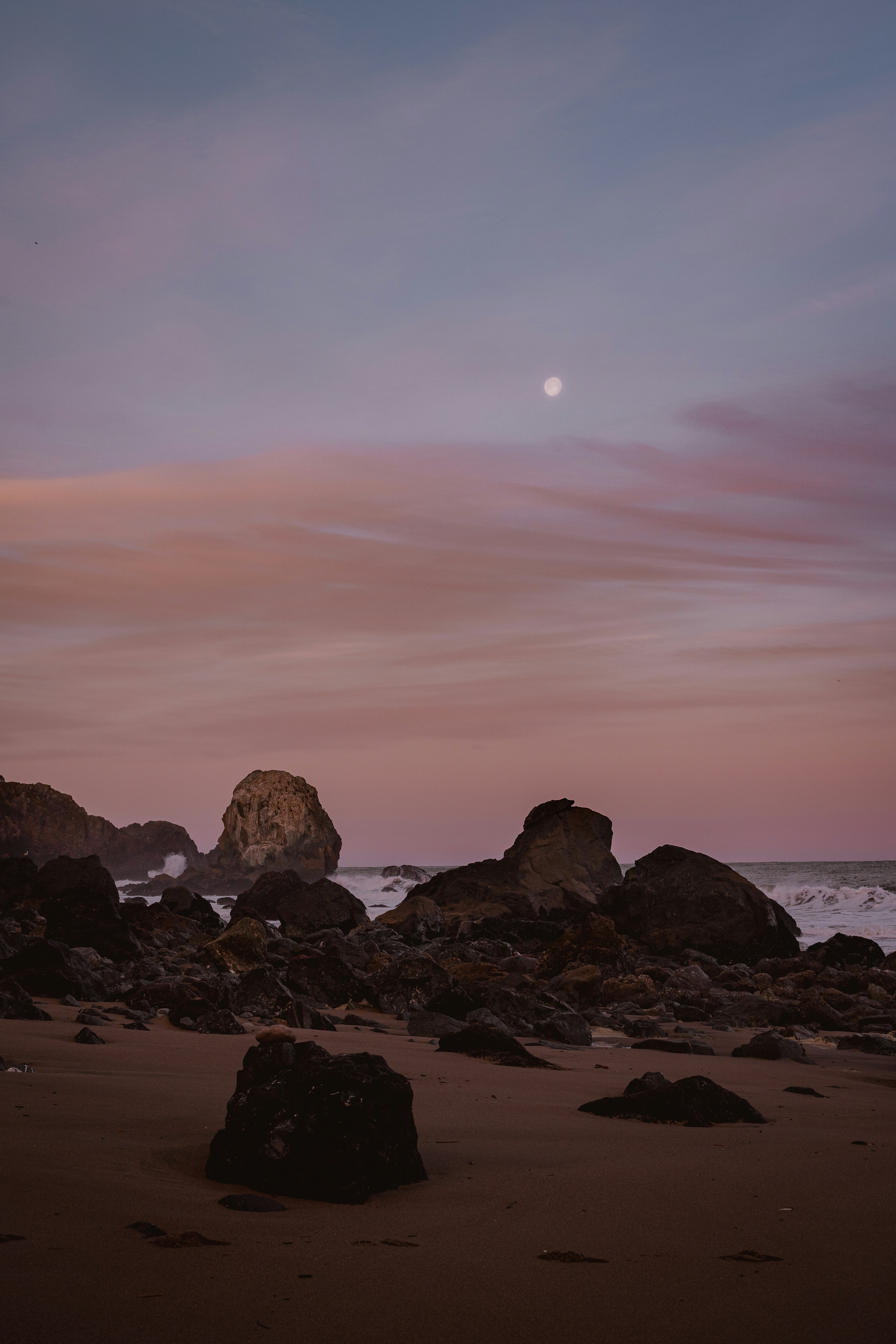 Foto zum Thema Ein Strand mit Felsen und einem Mond am Himmel ...