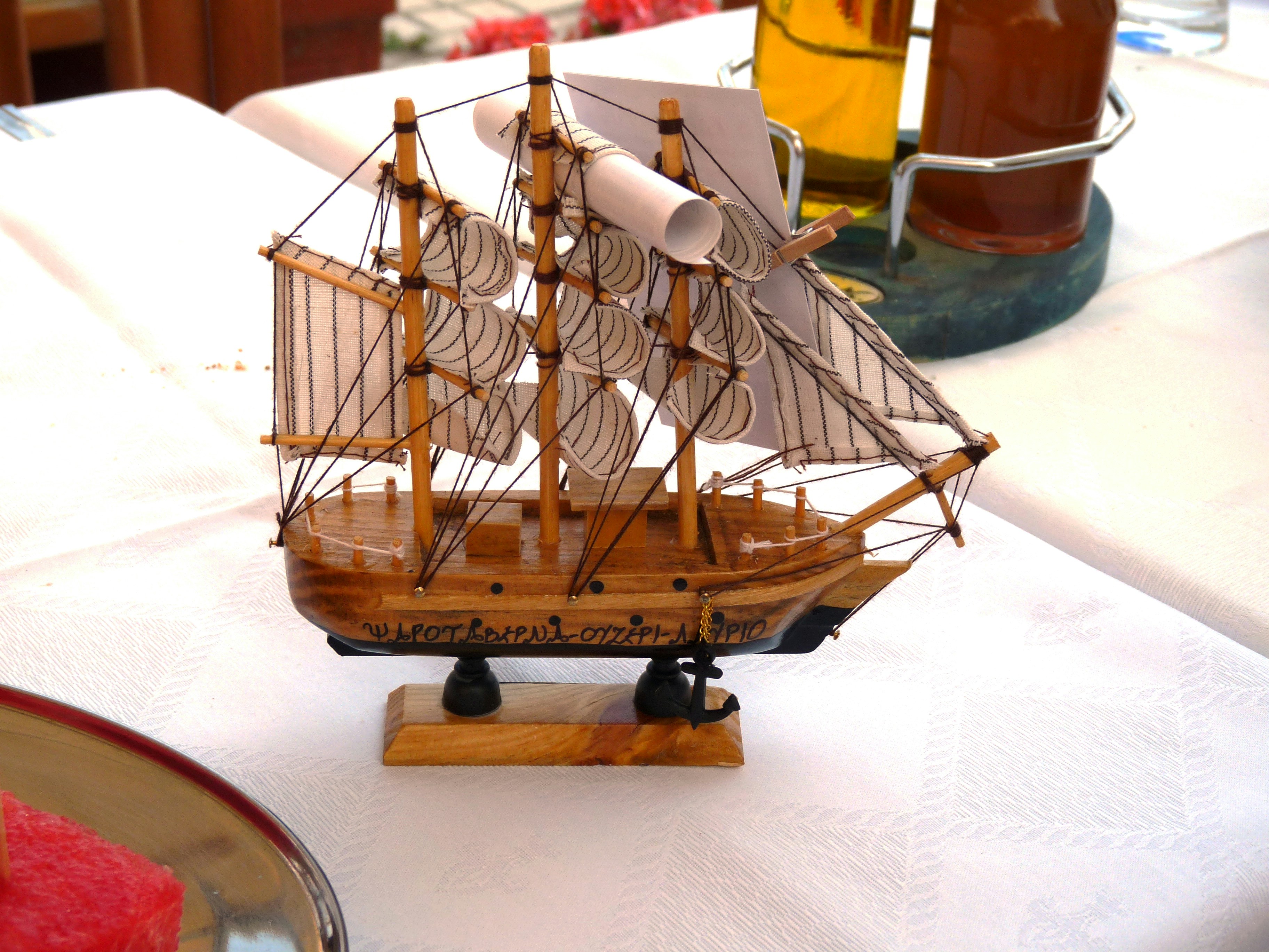 Intricately crafted wooden ship model with sails and rolled parchment, displayed on a dining table. The scene captures the essence of maritime artistry.