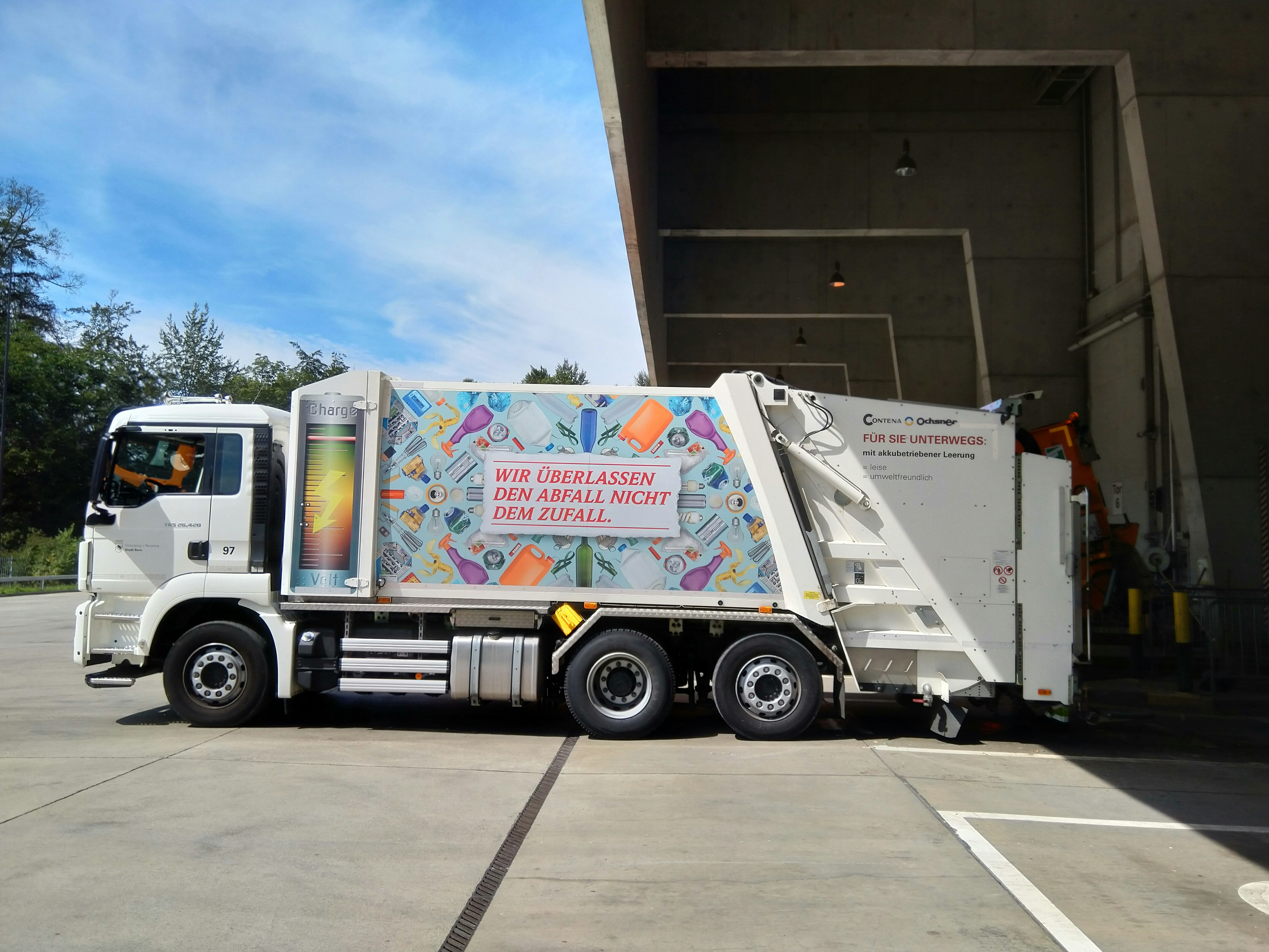 A garbage truck adorned with a colorful advertisement promoting waste management principles, parked under a large concrete structure.