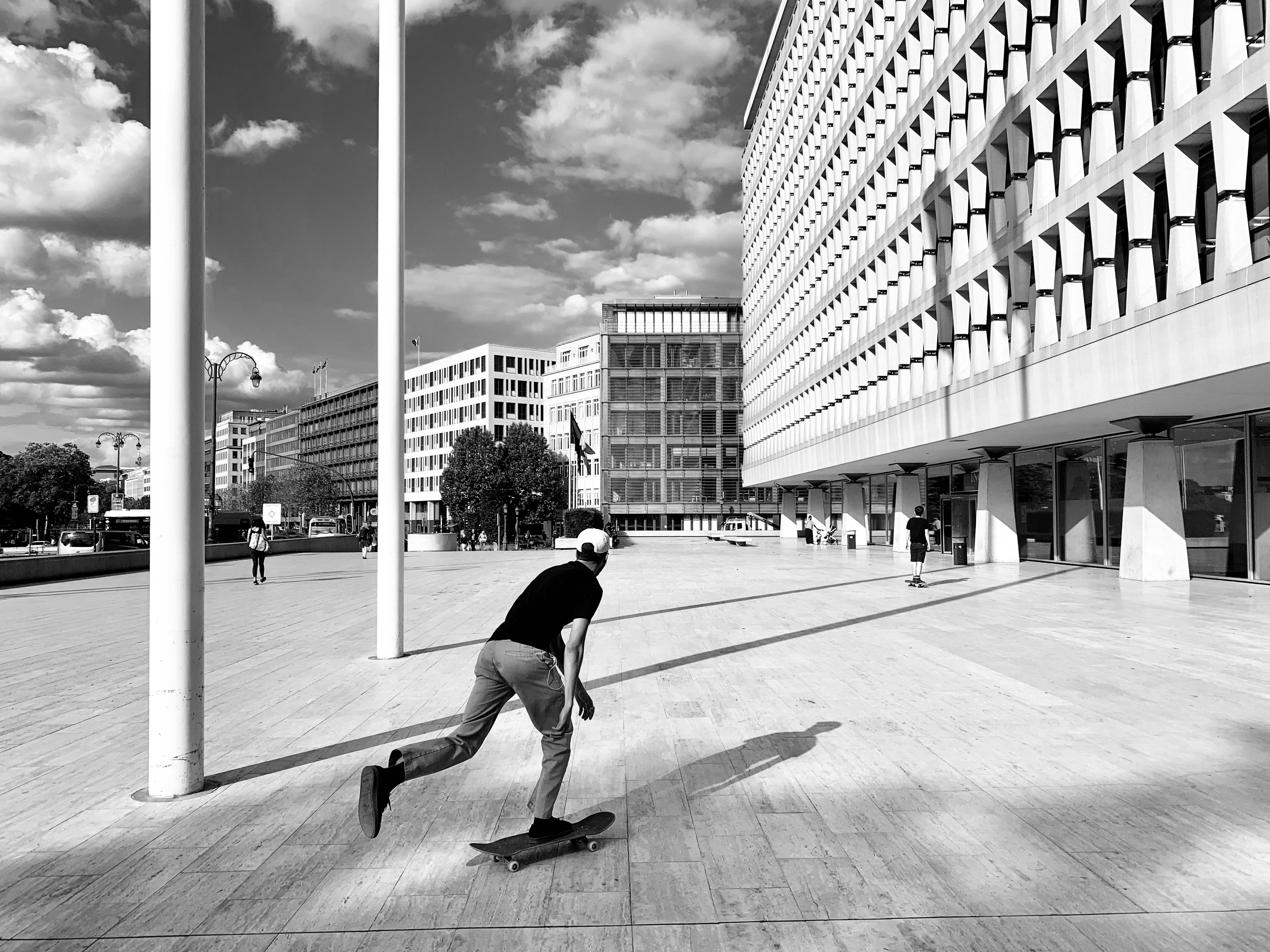 Skater gliding across a modern plaza, framed by sleek architecture and dynamic shadows. The scene captures the essence of urban life in motion.