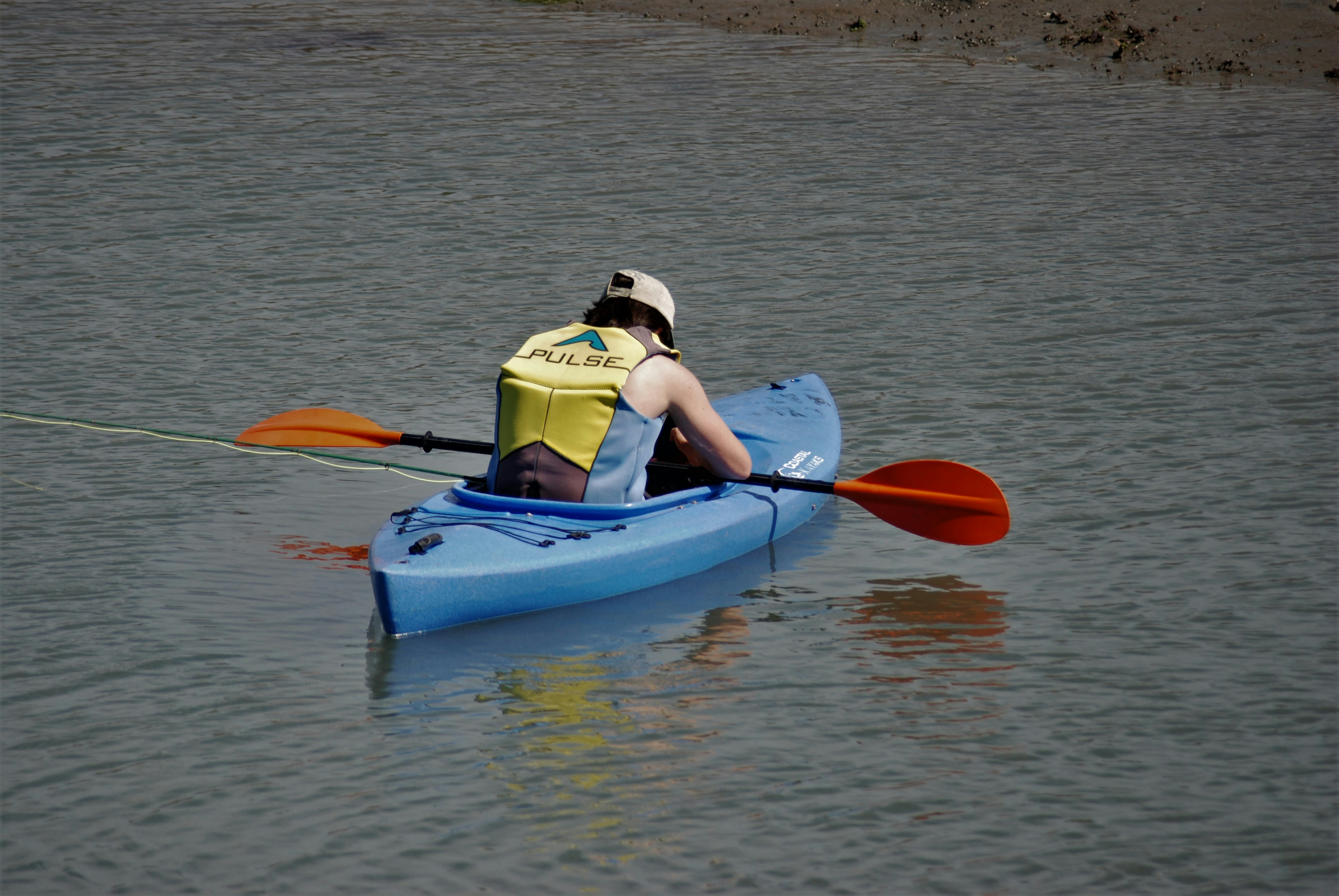 A kayaker in a blue kayak focuses intently on the water, surrounded by calm reflections. The scene captures a peaceful moment in nature.