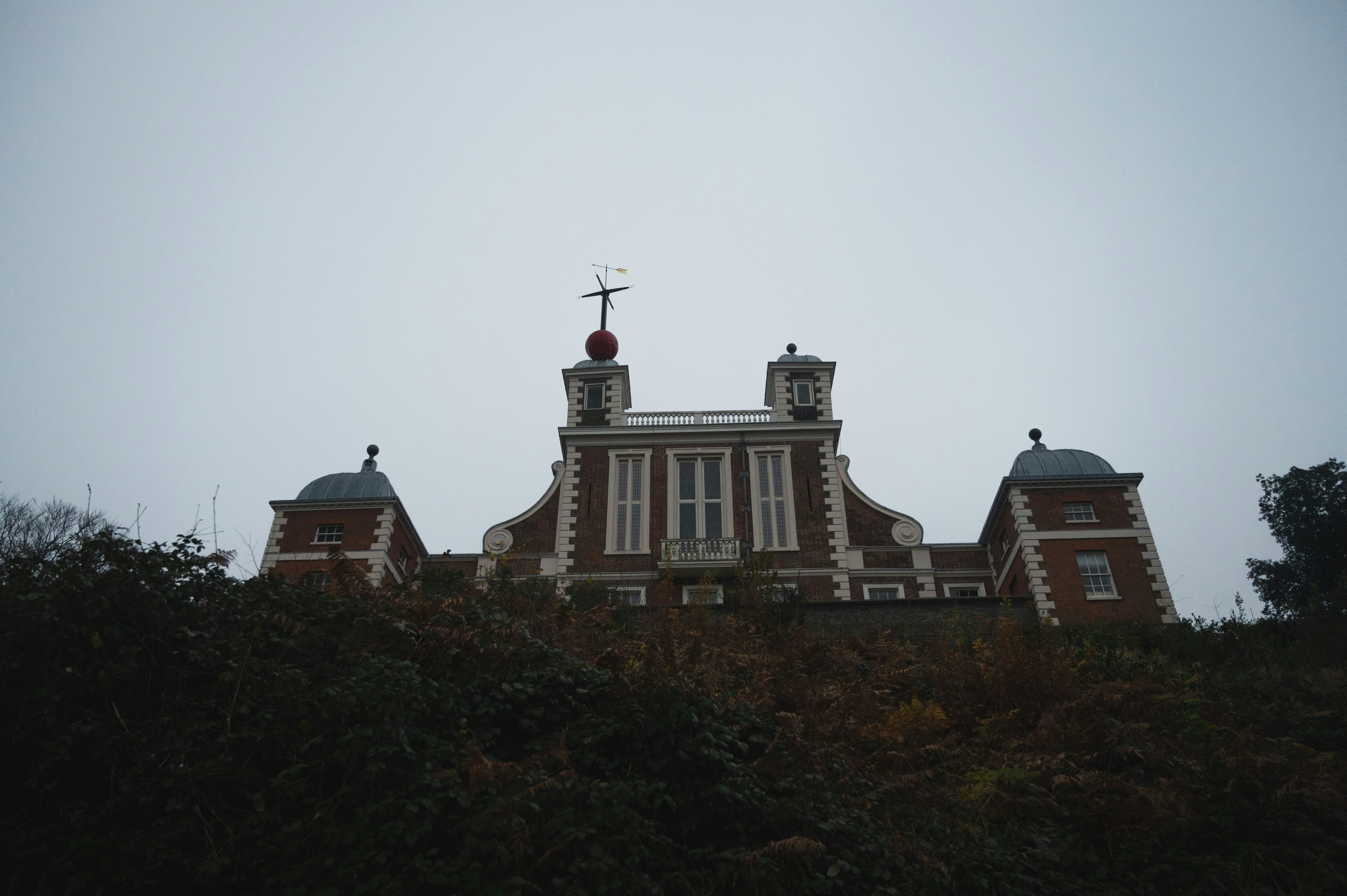 The Royal Observatory silhouetted against a muted winter sky, framed by dark foliage.