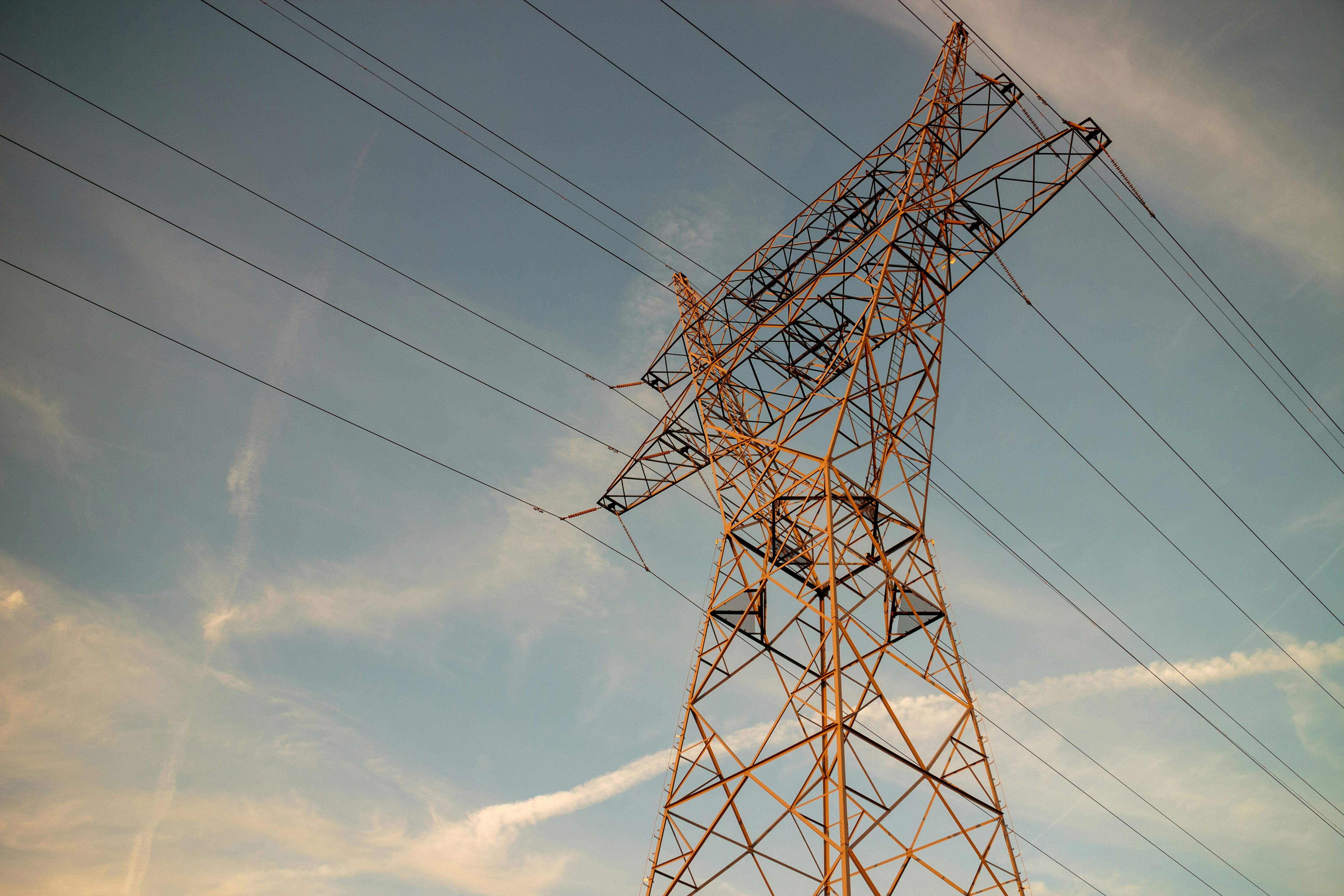 A towering power line structure against a pastel sky, highlighting the intricate design and engineering of electrical infrastructure.