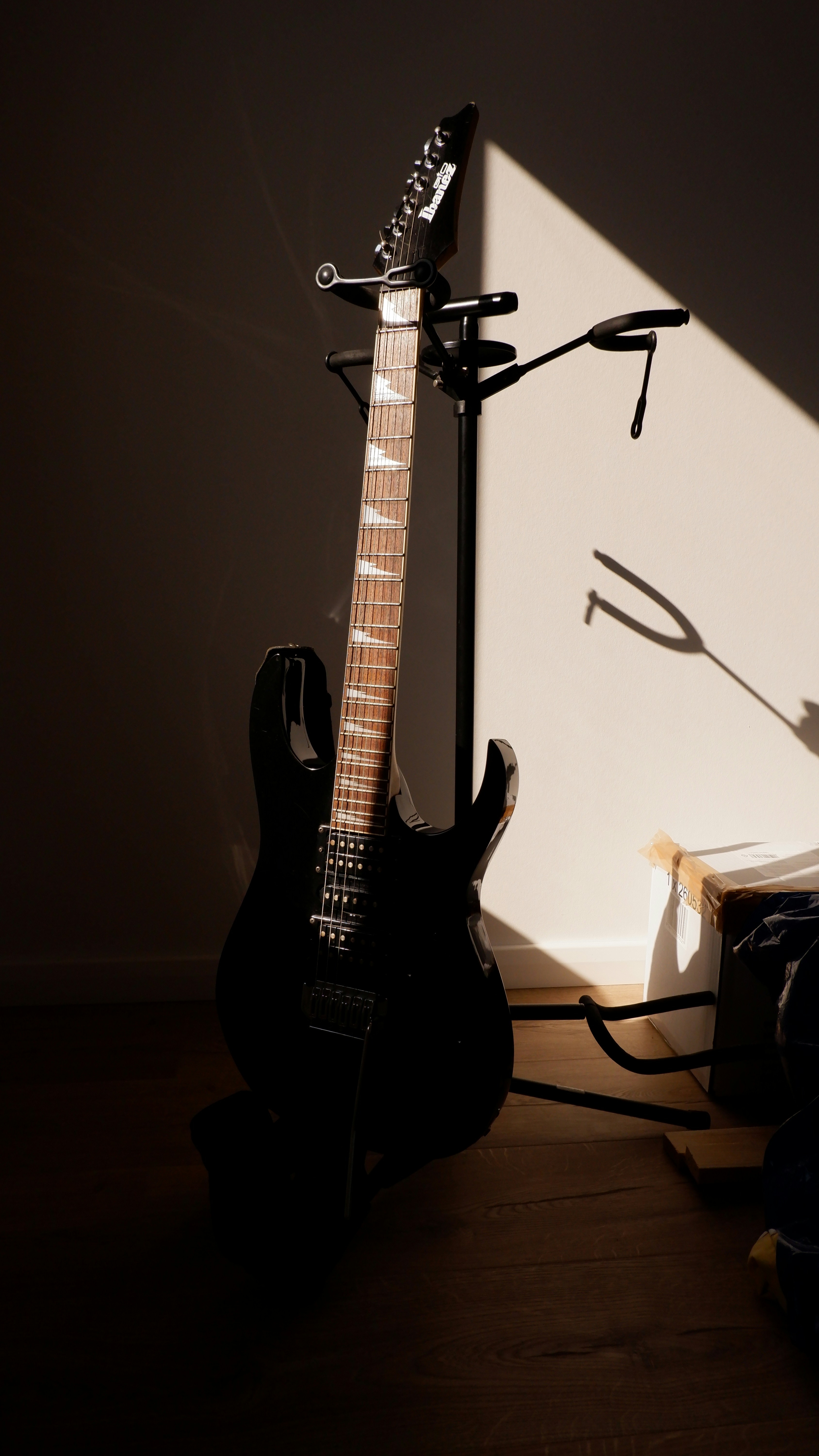 Black electric guitar resting on a stand, illuminated by soft light casting dramatic shadows on the wall.