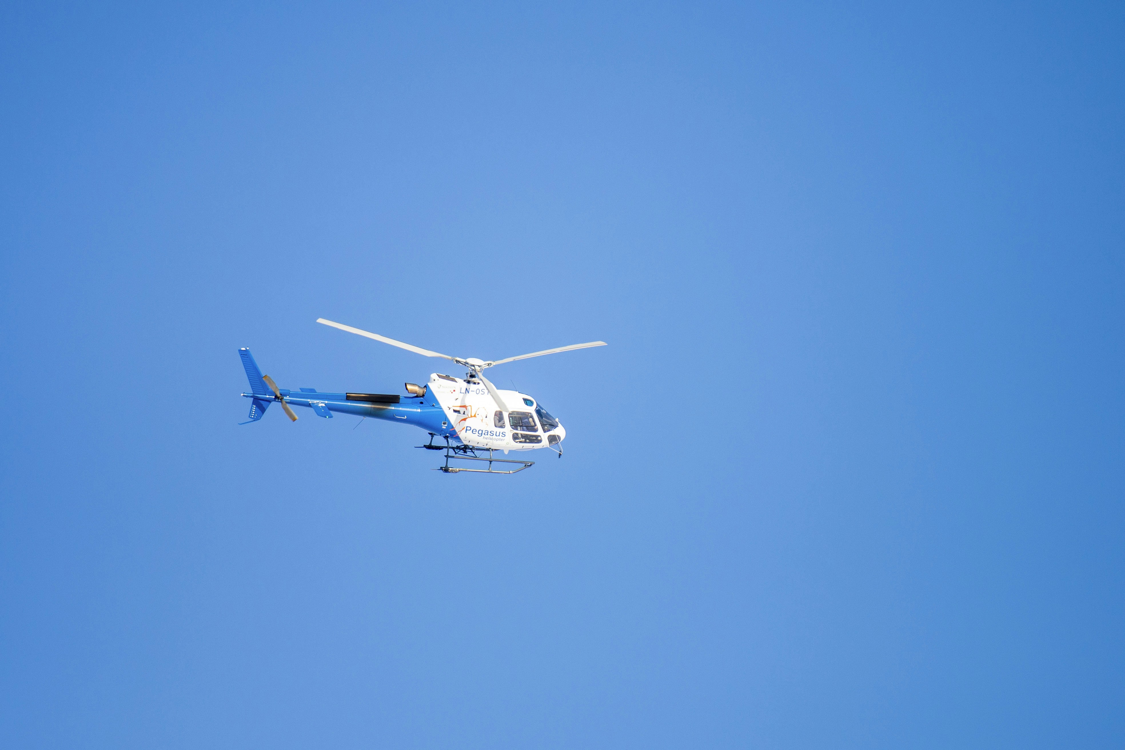 A blue and white helicopter flying through a blue sky photo – Free Blue ...