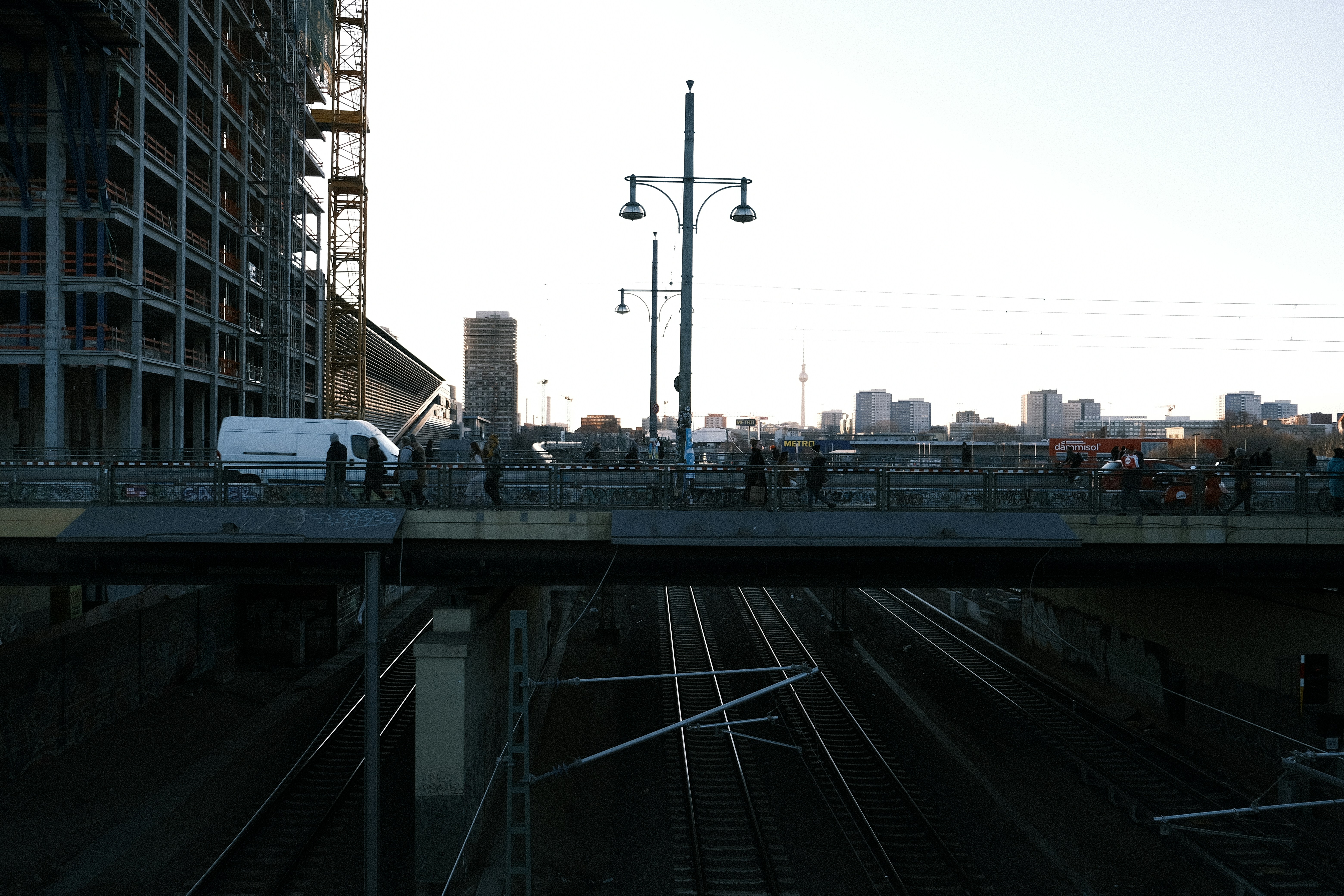 Construction site adjacent to a busy railway bridge with pedestrians and vehicles traversing the urban landscape.