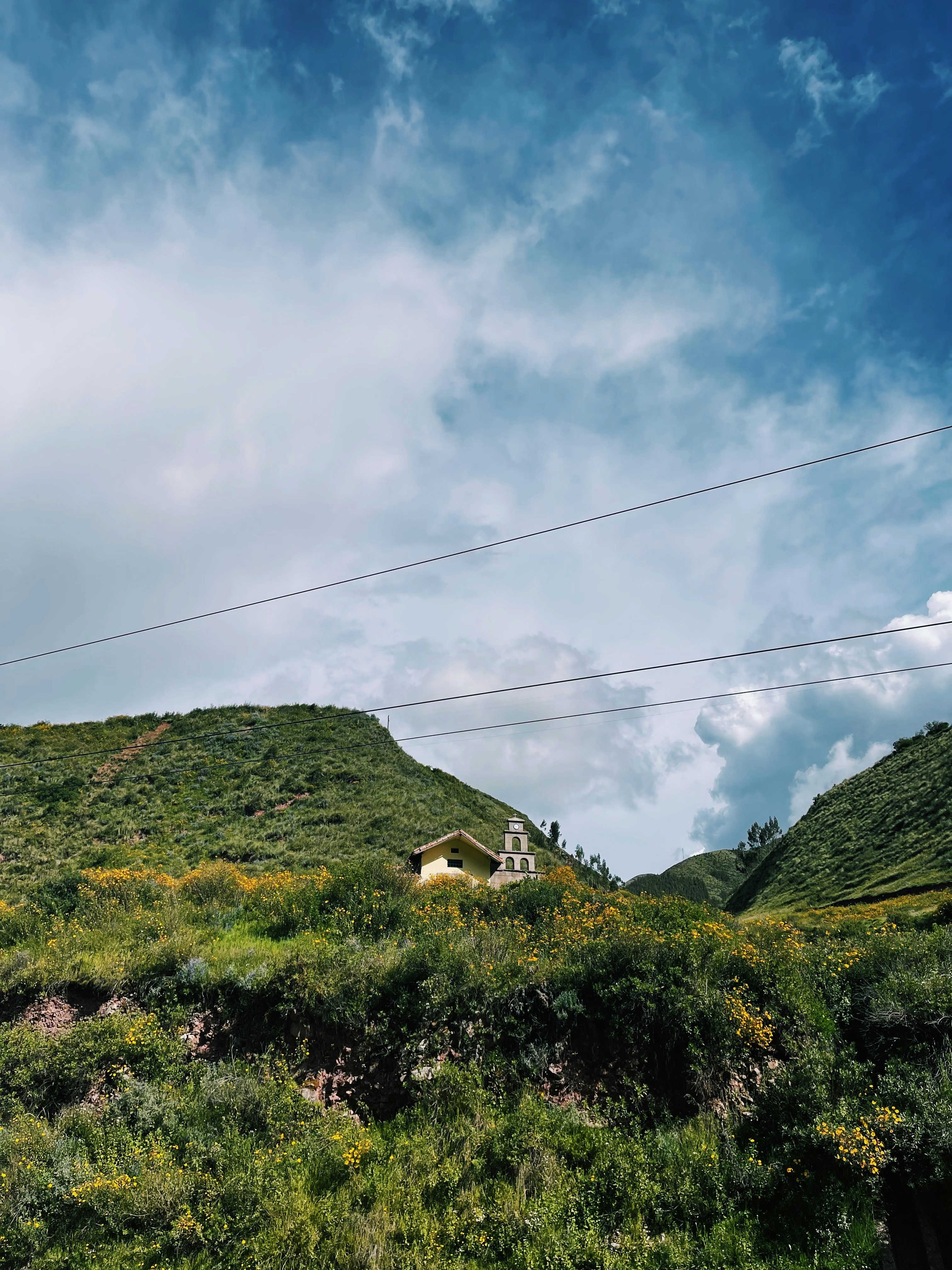 A quaint yellow house nestled among lush green hills under a dramatic sky, showcasing the harmony between architecture and nature.