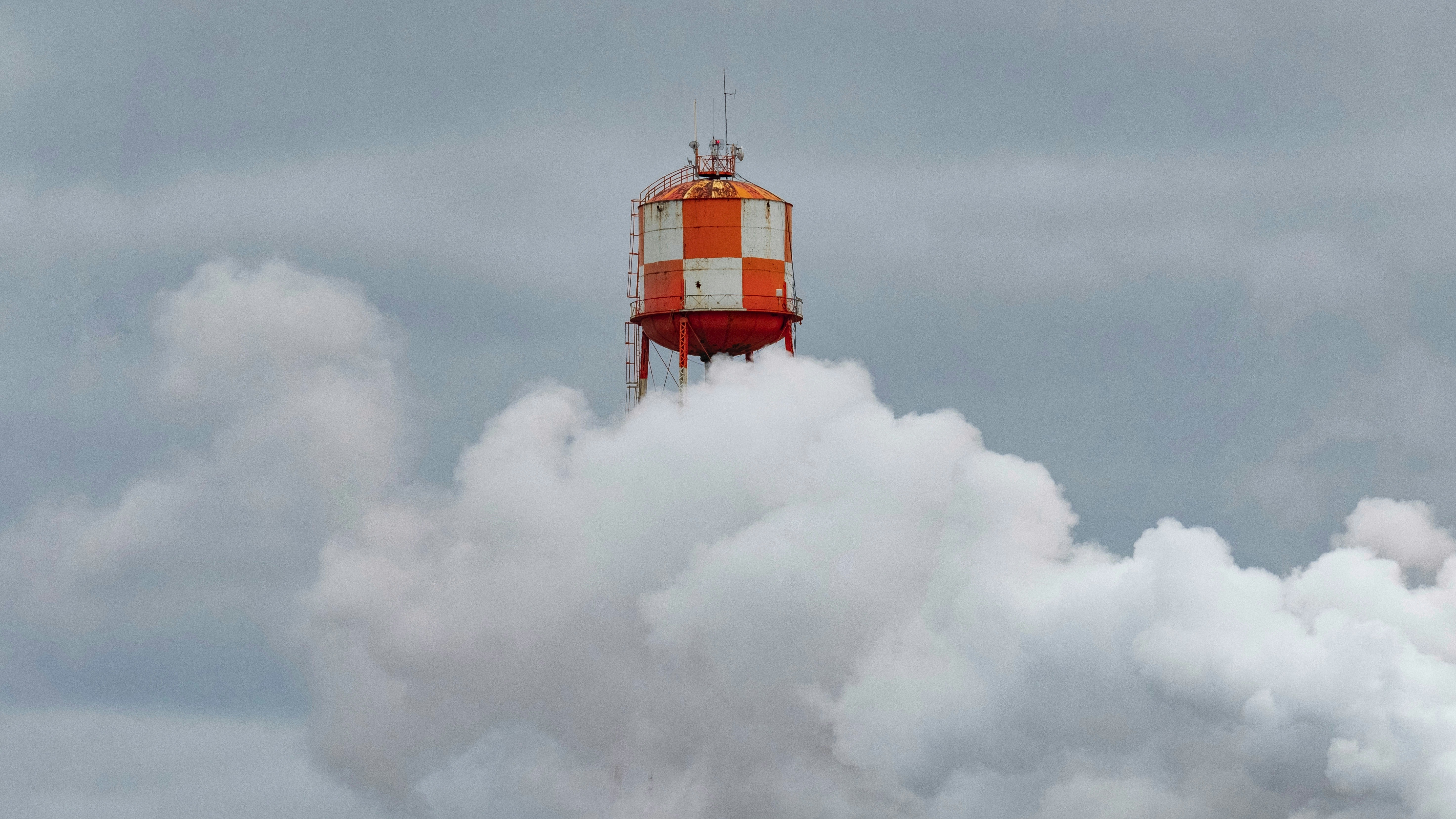 Orange and white lighthouse emerging from dense clouds against a gray sky.