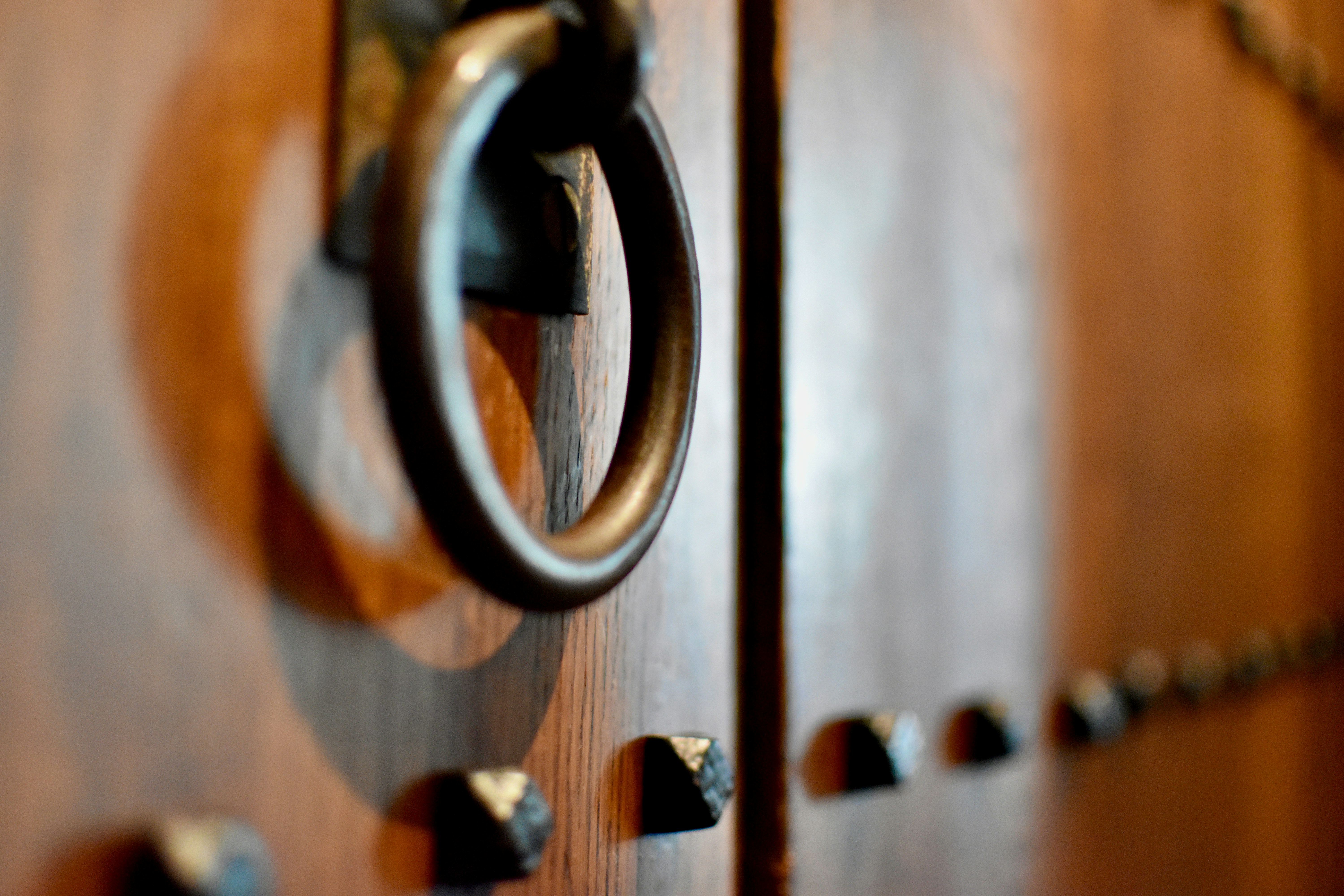 Close-up of a vintage door knocker set against a wooden door adorned with decorative studs.