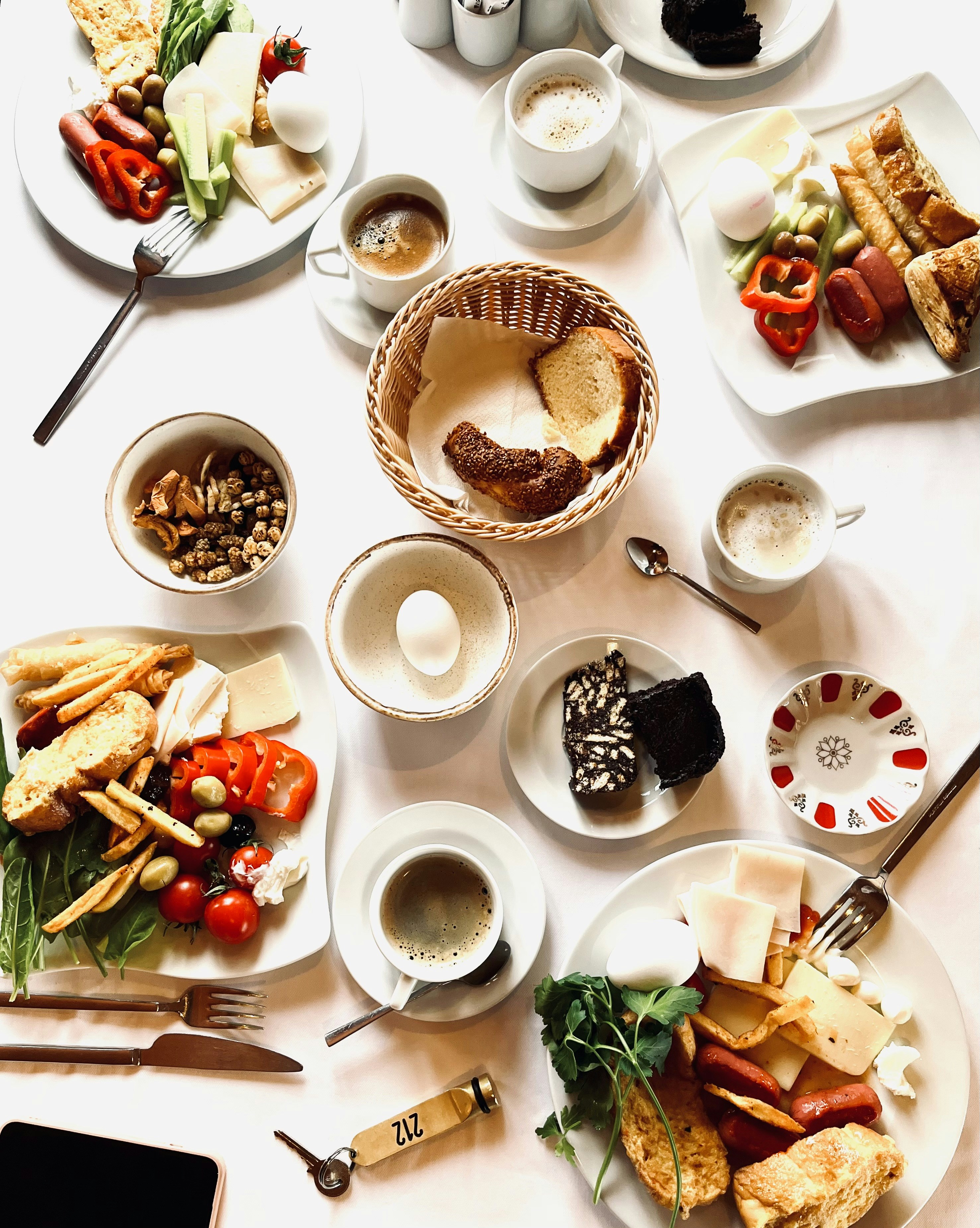 Variety of breakfast dishes displayed on a table, featuring eggs, fresh vegetables, and pastries. A basket of bread and cups of coffee complement the spread.