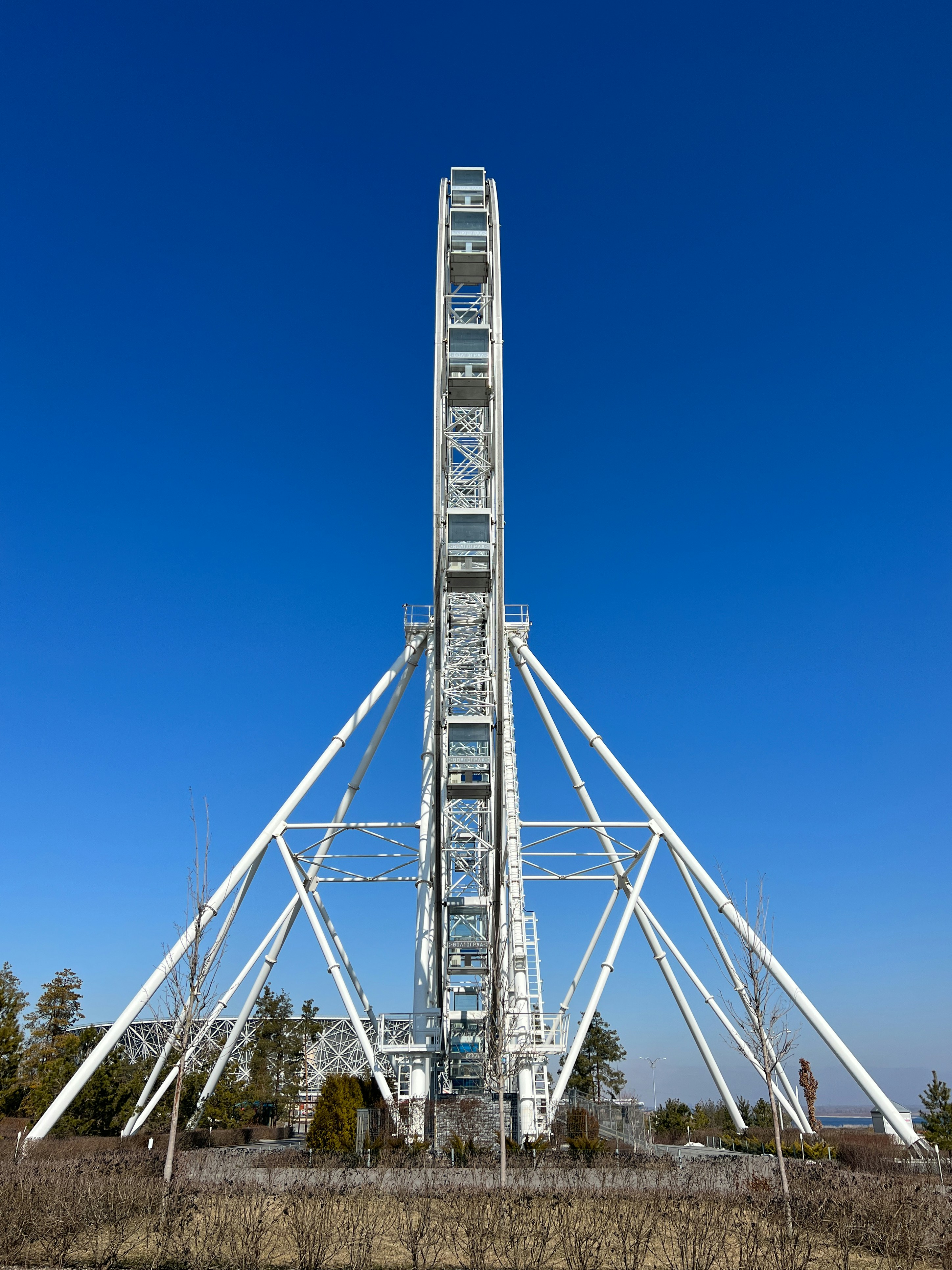 A towering Ferris wheel rises against a clear blue sky, showcasing its intricate support structure and glass cabins.