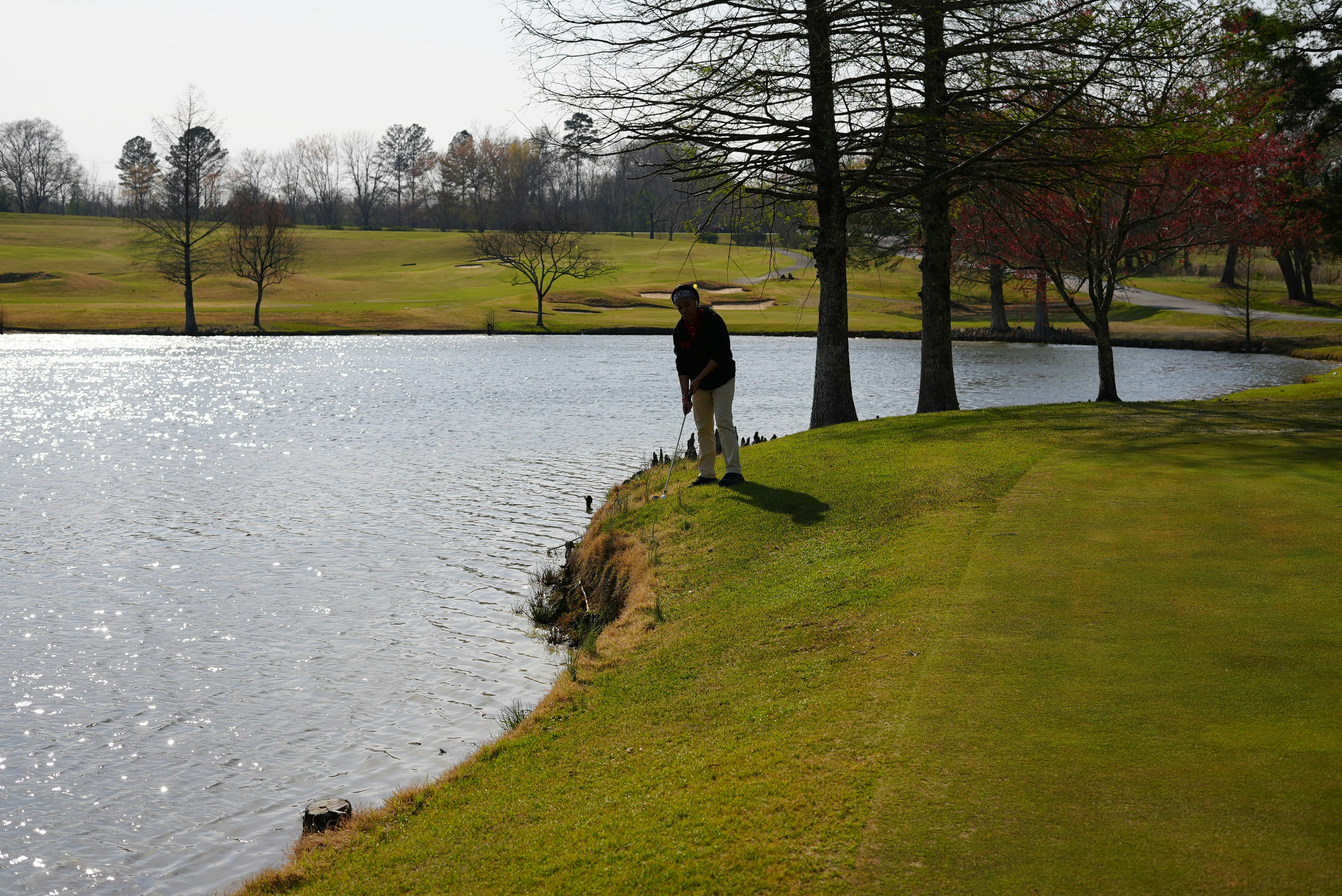 Lone golfer at the edge: calm light, edge of a lake
