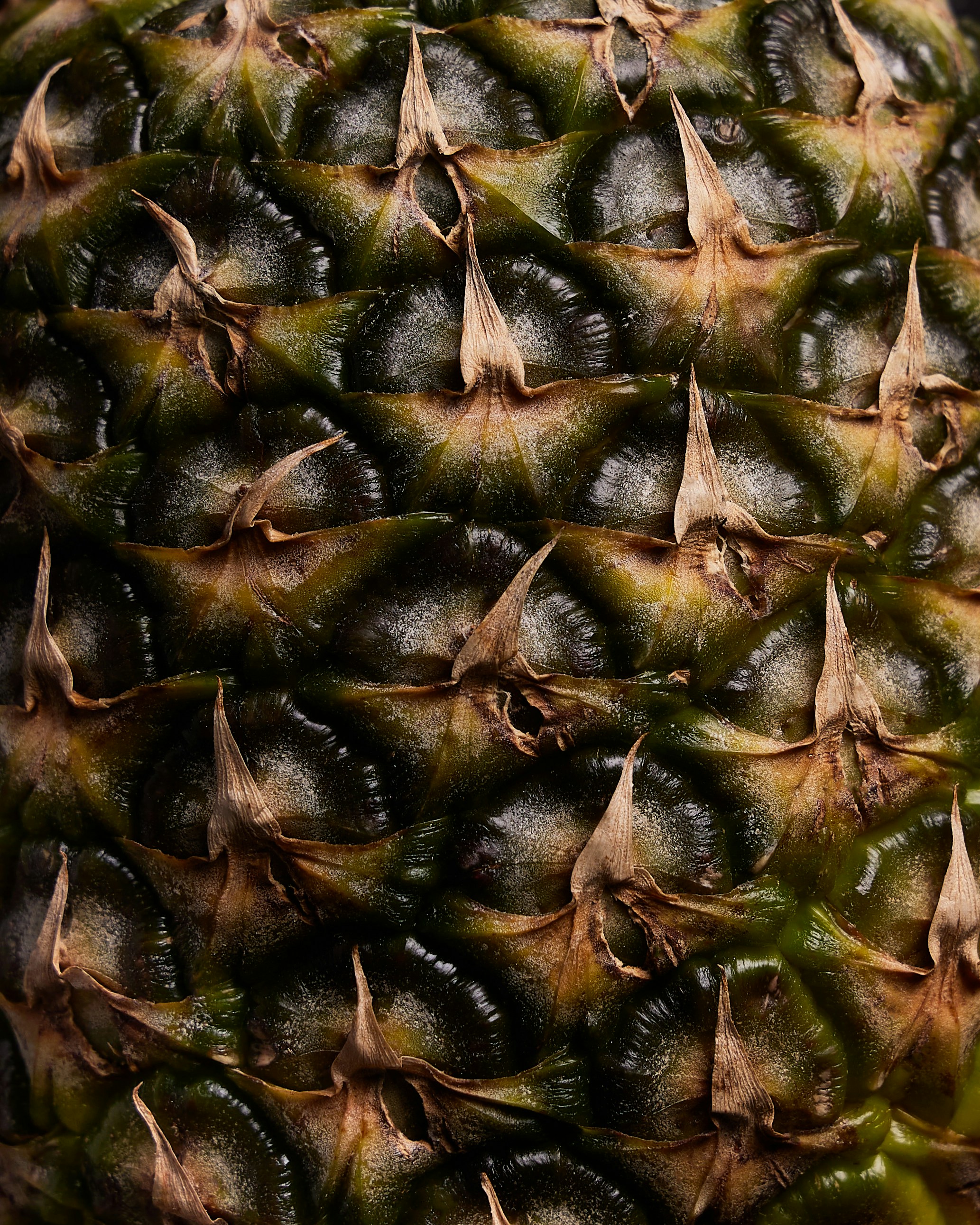 Close-up of a pineapple's textured skin, revealing intricate patterns and natural colors. The image highlights the unique details of the fruit's exterior.