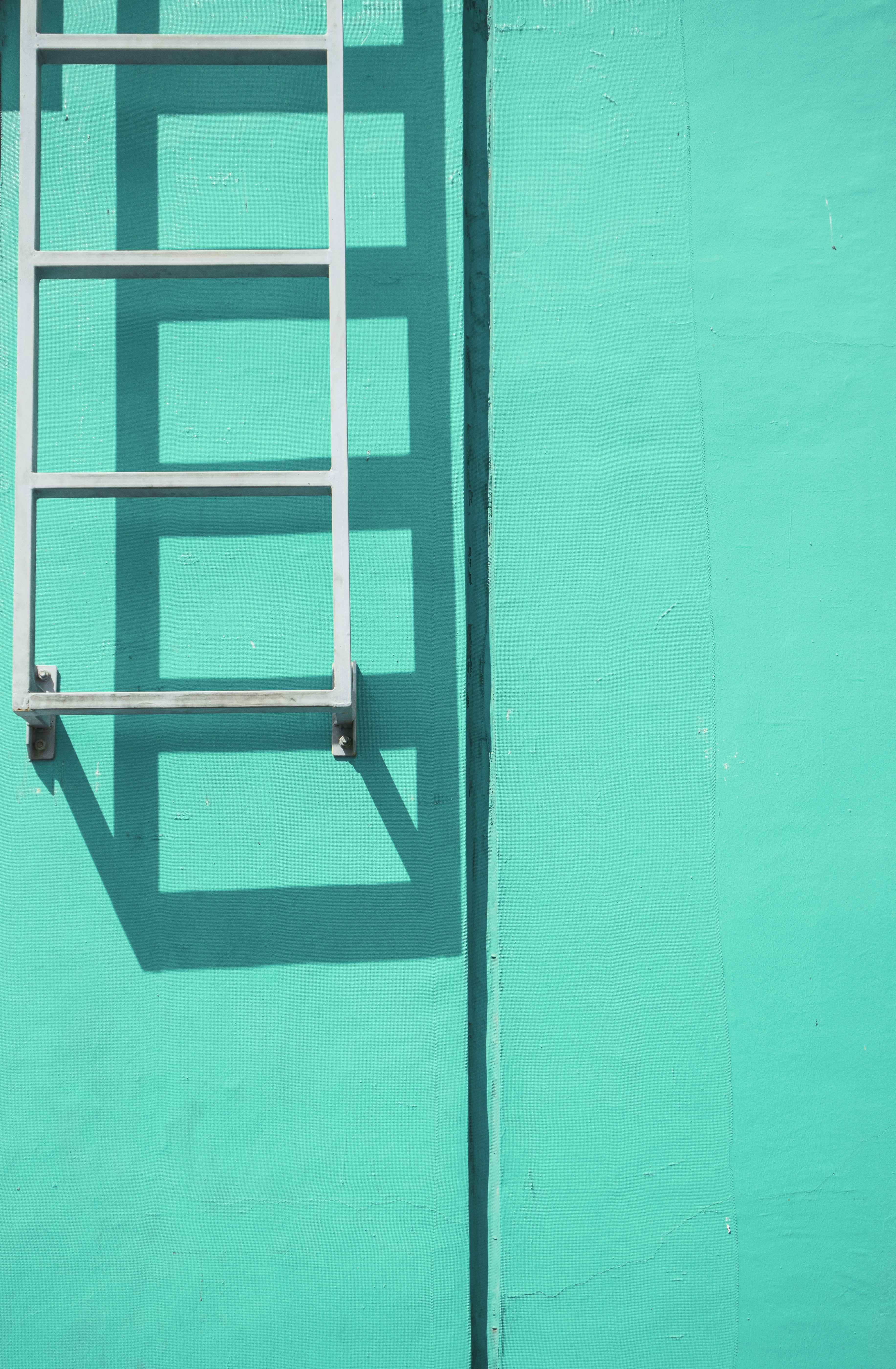 Teal Facade Geometry: A Ladder Casts Precise Shadows on a Sunlit Wall