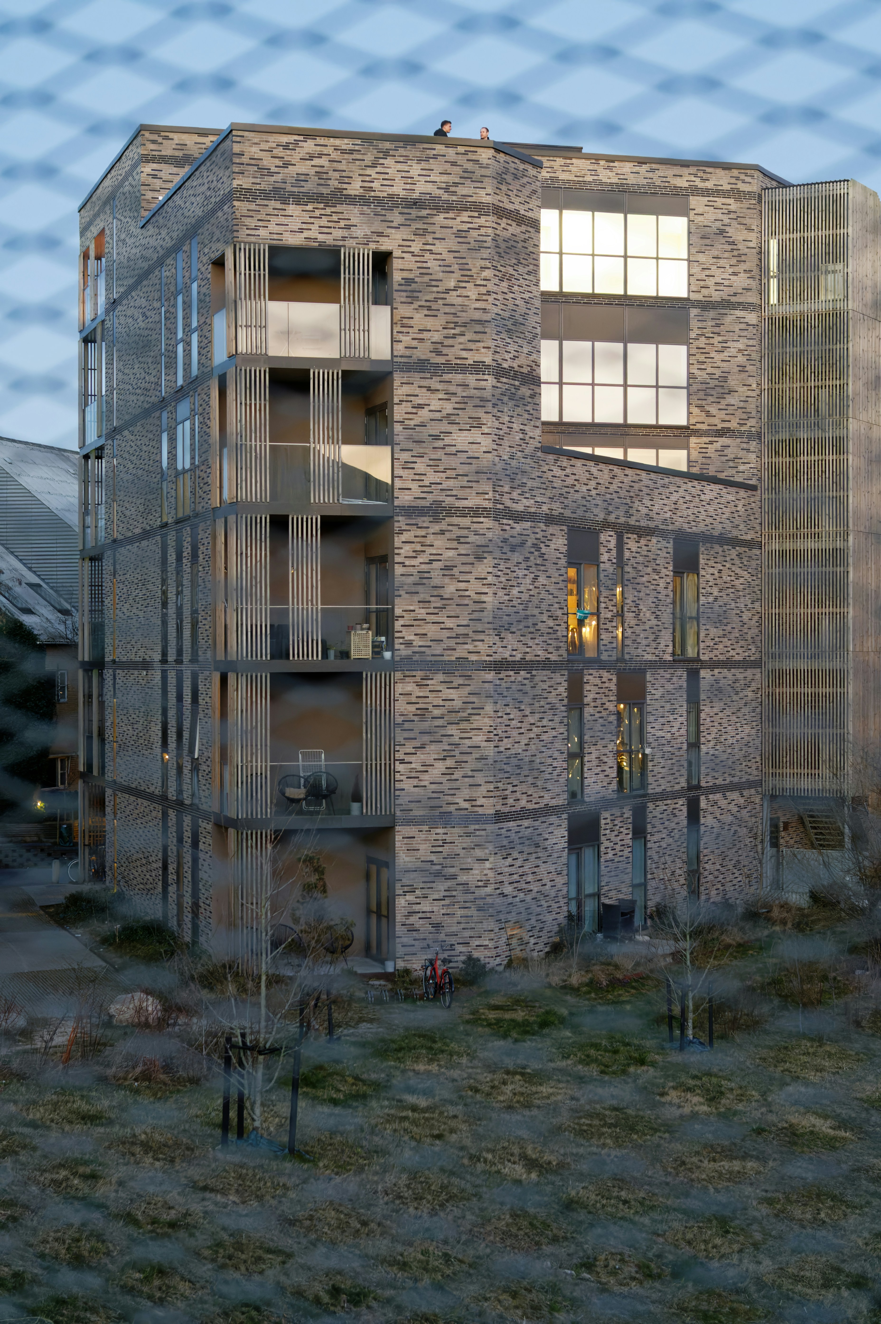 Contemporary building with textured brick facade and large windows, surrounded by greenery and urban elements. Evening light enhances the architectural features.