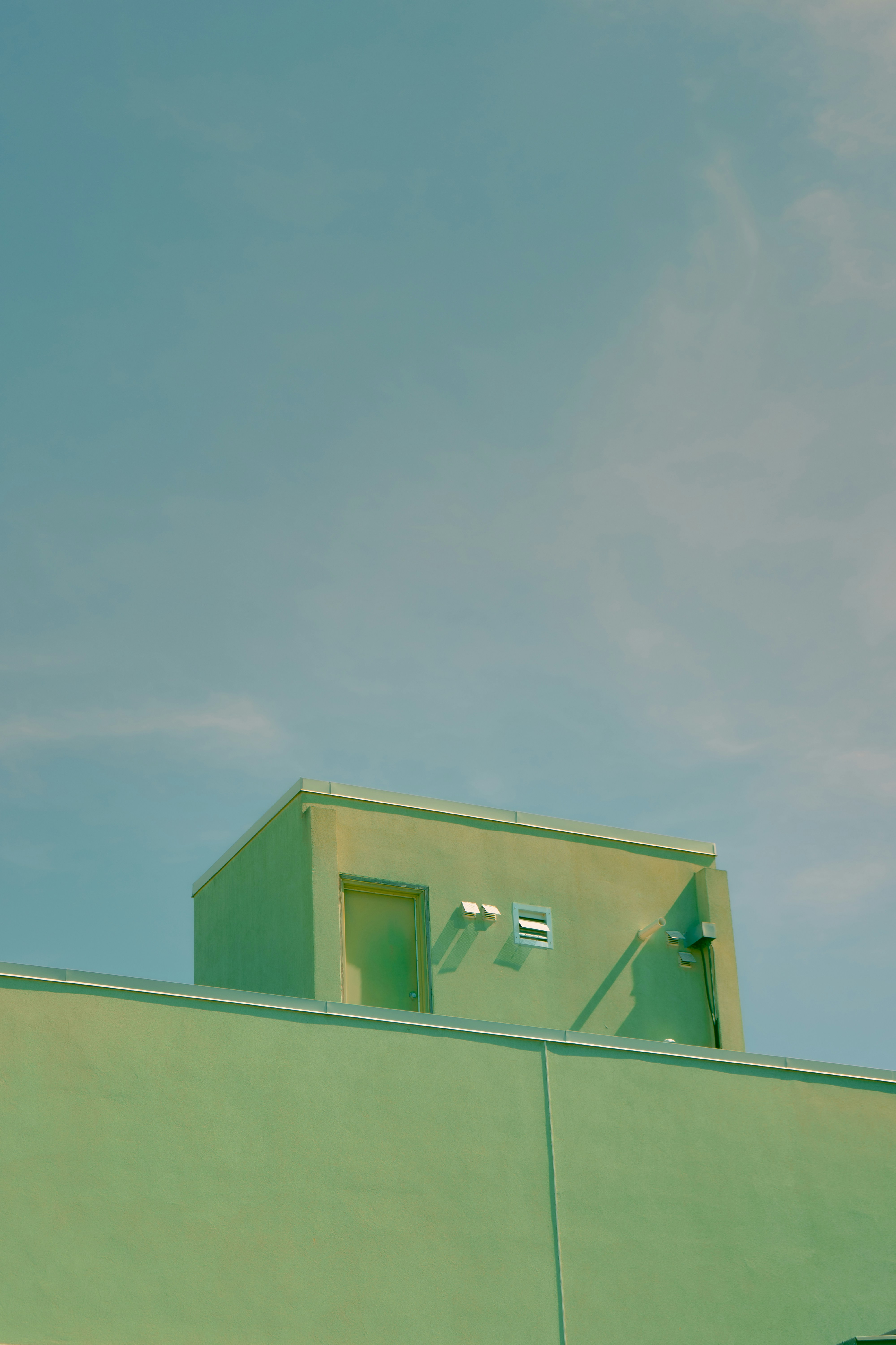 Minimalist green structure against a clear sky, showcasing contemporary design elements. A striking contrast between the building and the atmosphere.