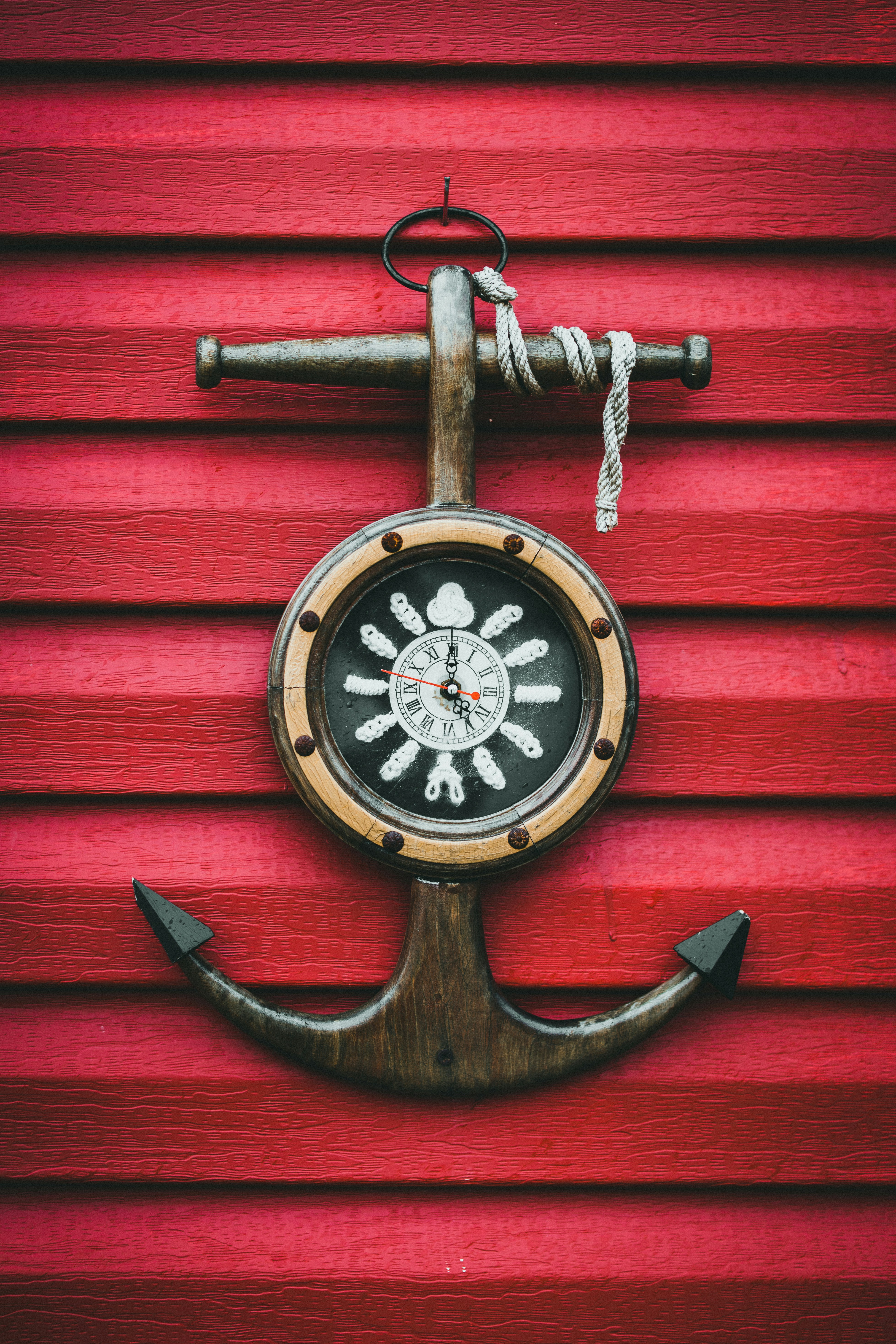 Vintage anchor clock mounted on a vibrant red wooden wall, showcasing nautical themes and craftsmanship.
