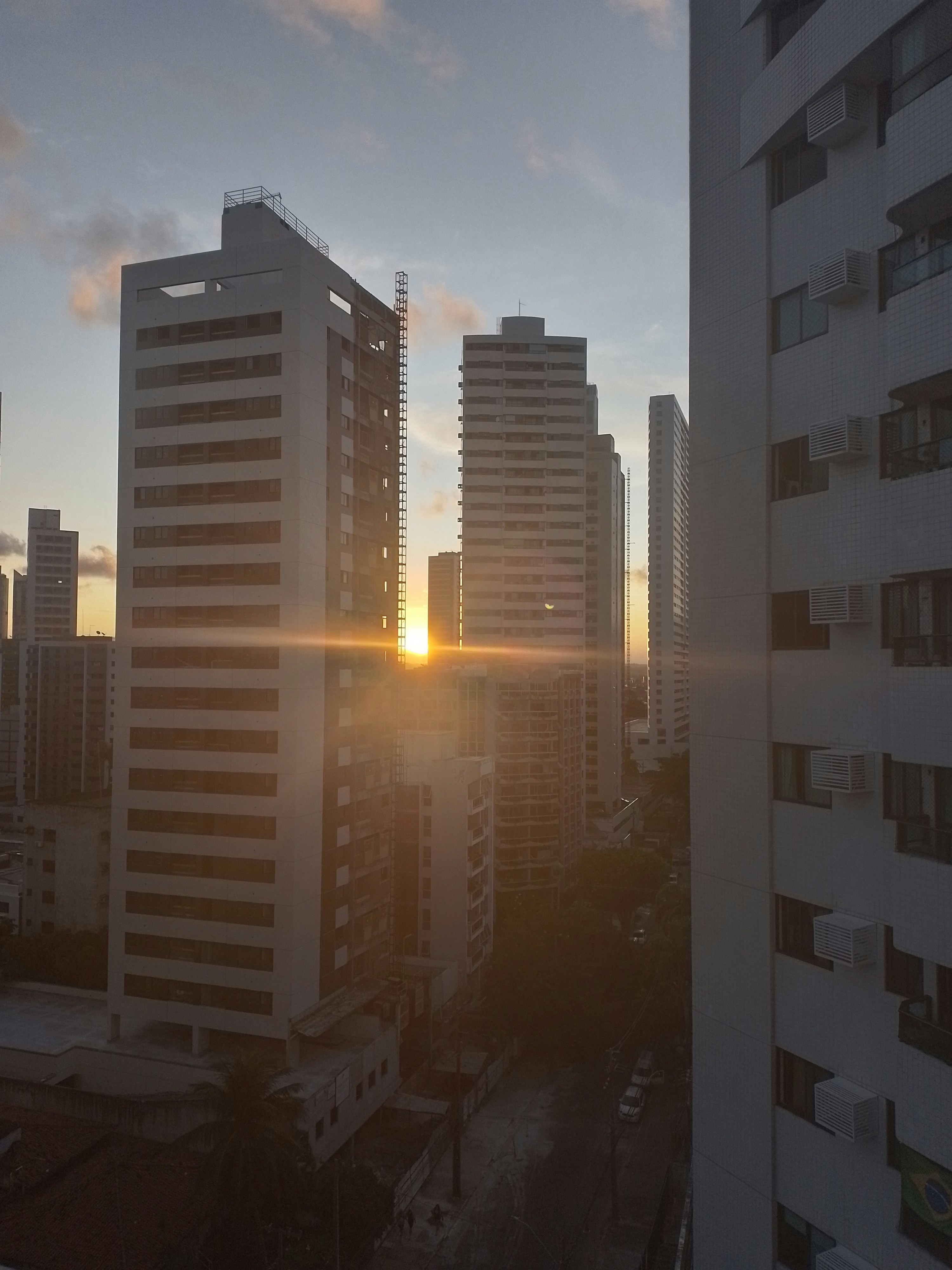 Golden sunset peeking through towering skyscrapers in a bustling cityscape, highlighting the interplay of light and architecture.