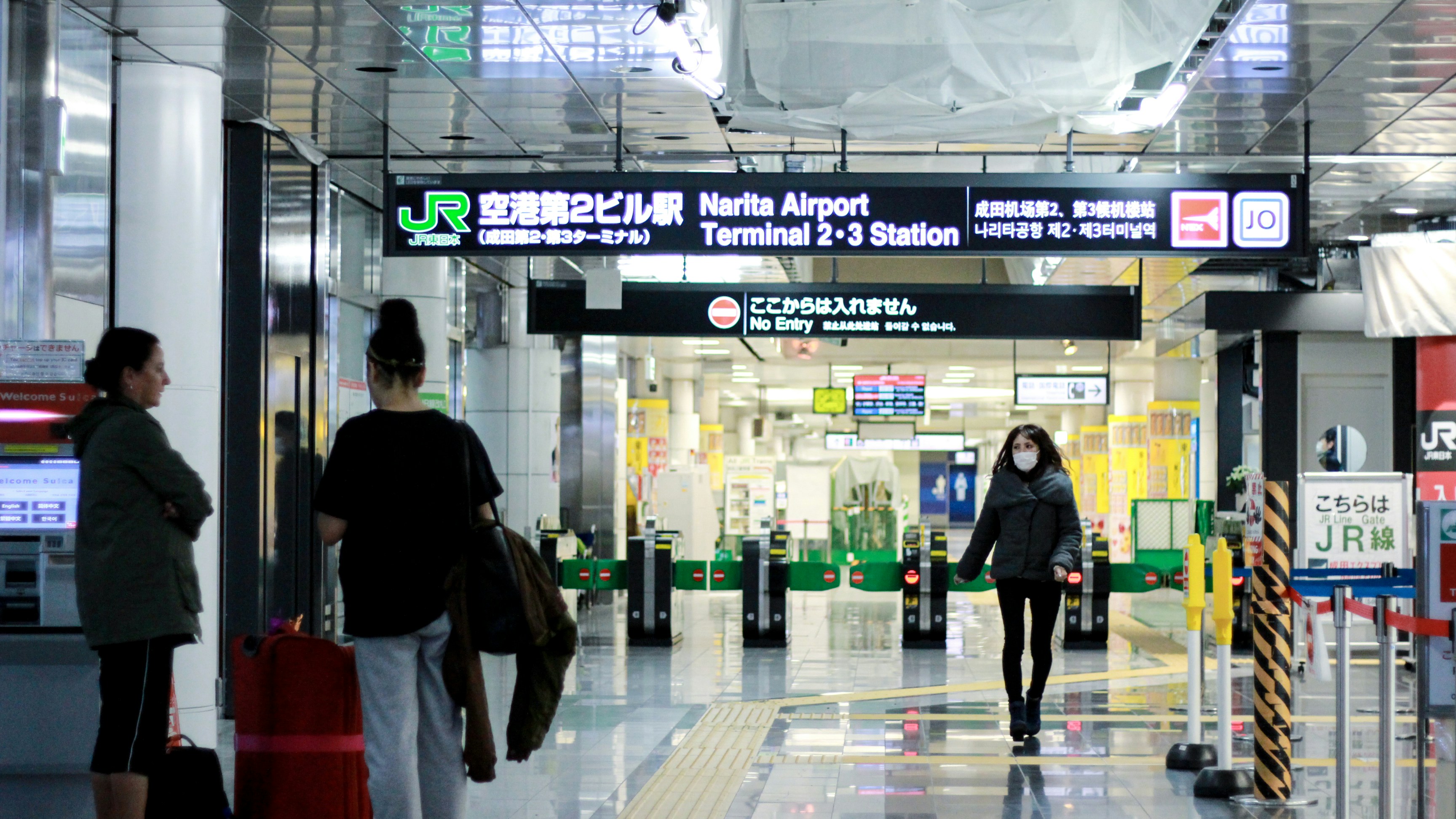 Travelers navigate a brightly lit airport terminal with prominent signage overhead.