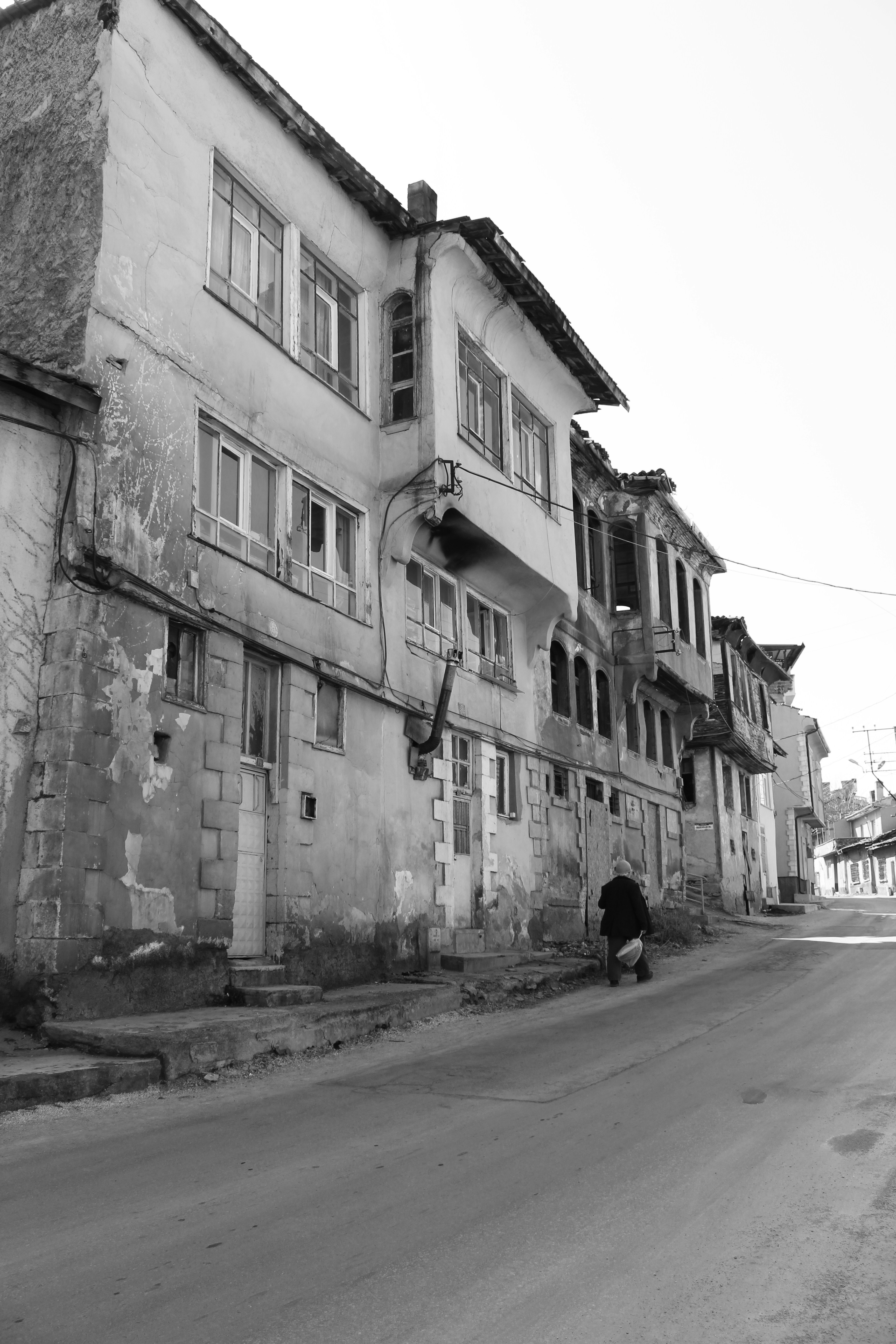 Weathered buildings line a narrow street, showcasing peeling paint and intricate architecture. A solitary figure walks past, adding a sense of scale and nostalgia.
