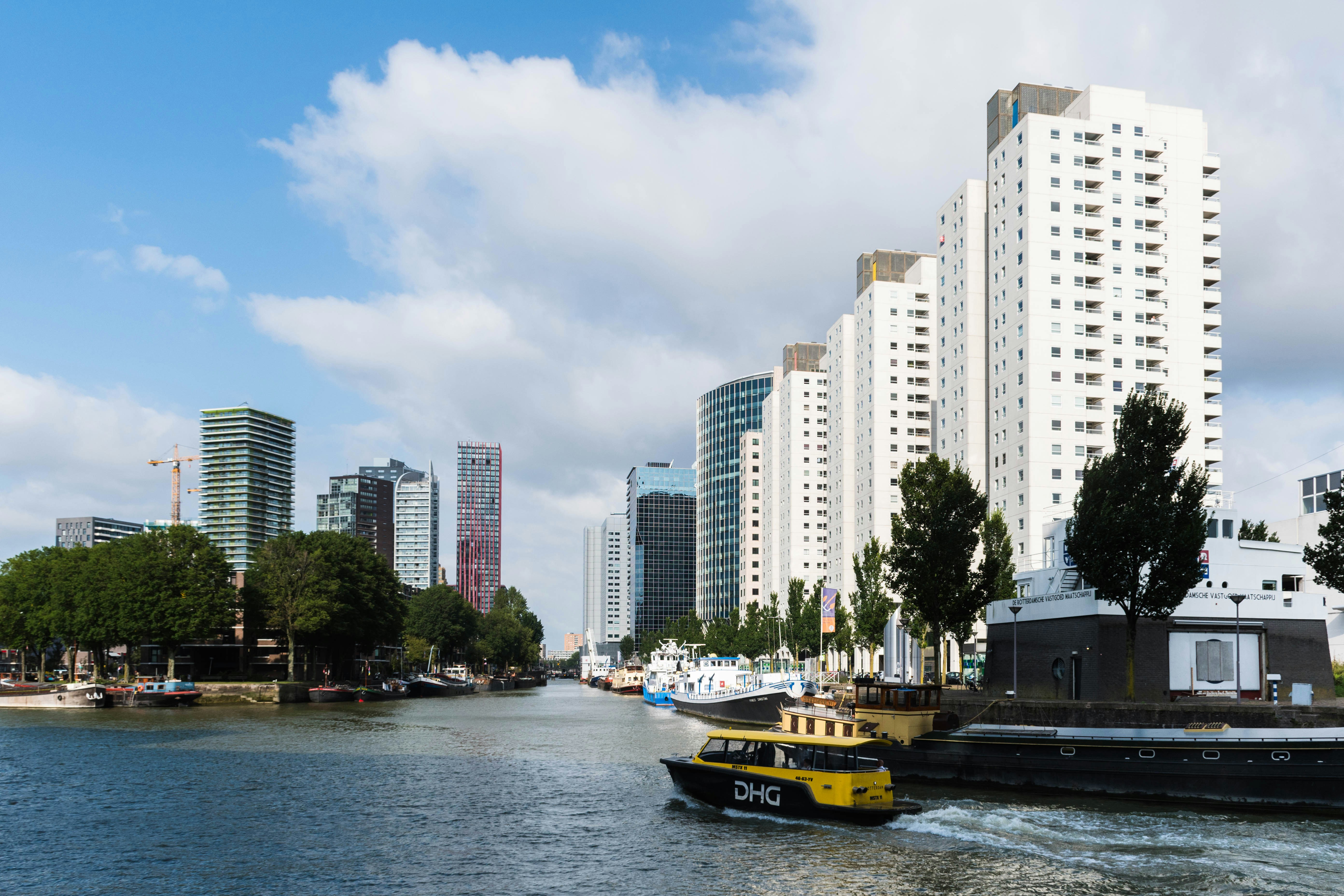 Yellow boat cruising along a river beside modern high-rise buildings under a partly cloudy sky.