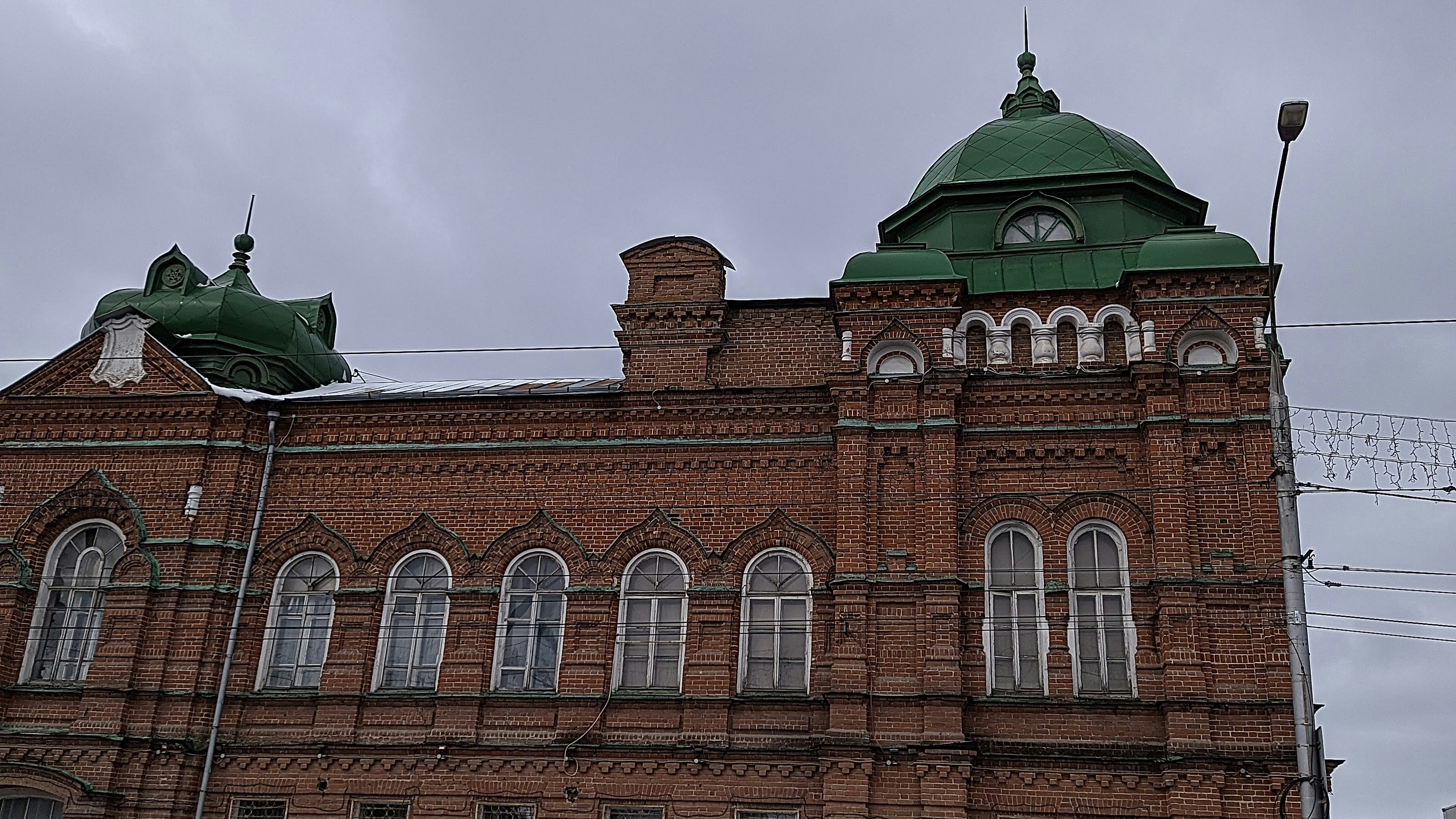 Ornate brick building with green domes and arched windows against a cloudy sky.