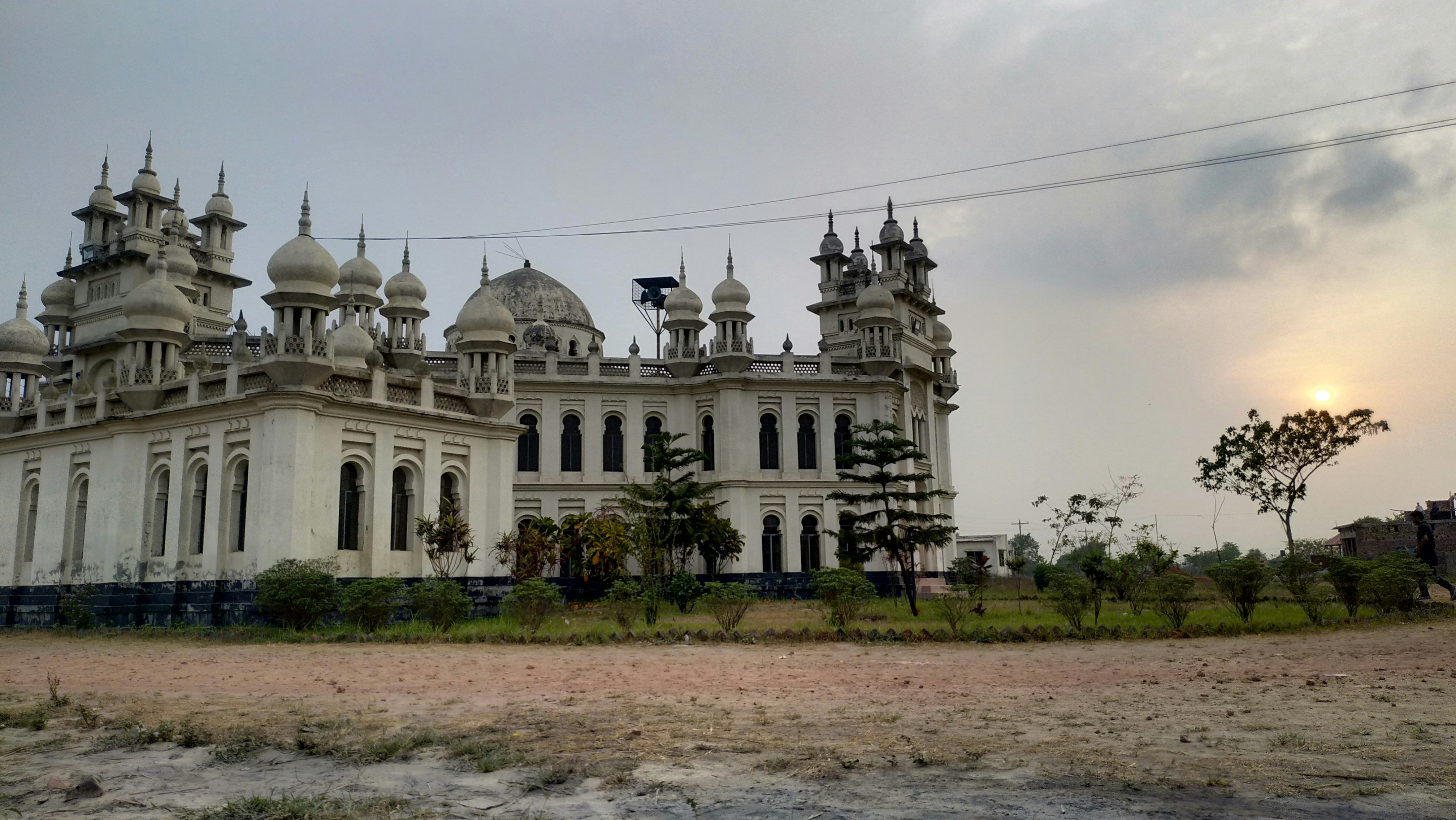 Intricate white palace with ornate domes and towers, set against a dusky sky. The fading sunlight casts a warm glow on the structure.
