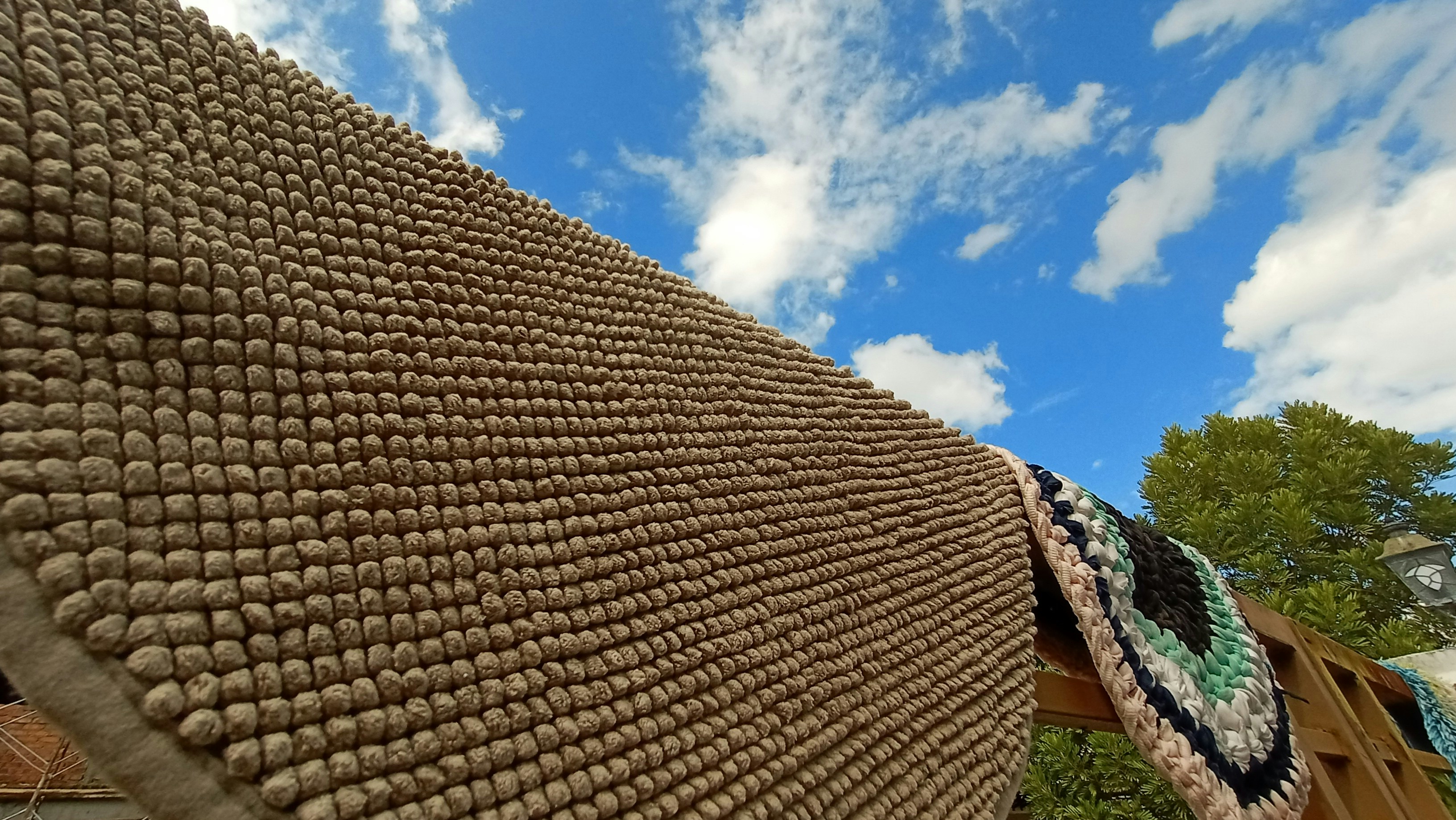 Close-up of intricately woven rugs hanging on a wooden frame, set against a backdrop of vibrant blue sky and fluffy clouds.