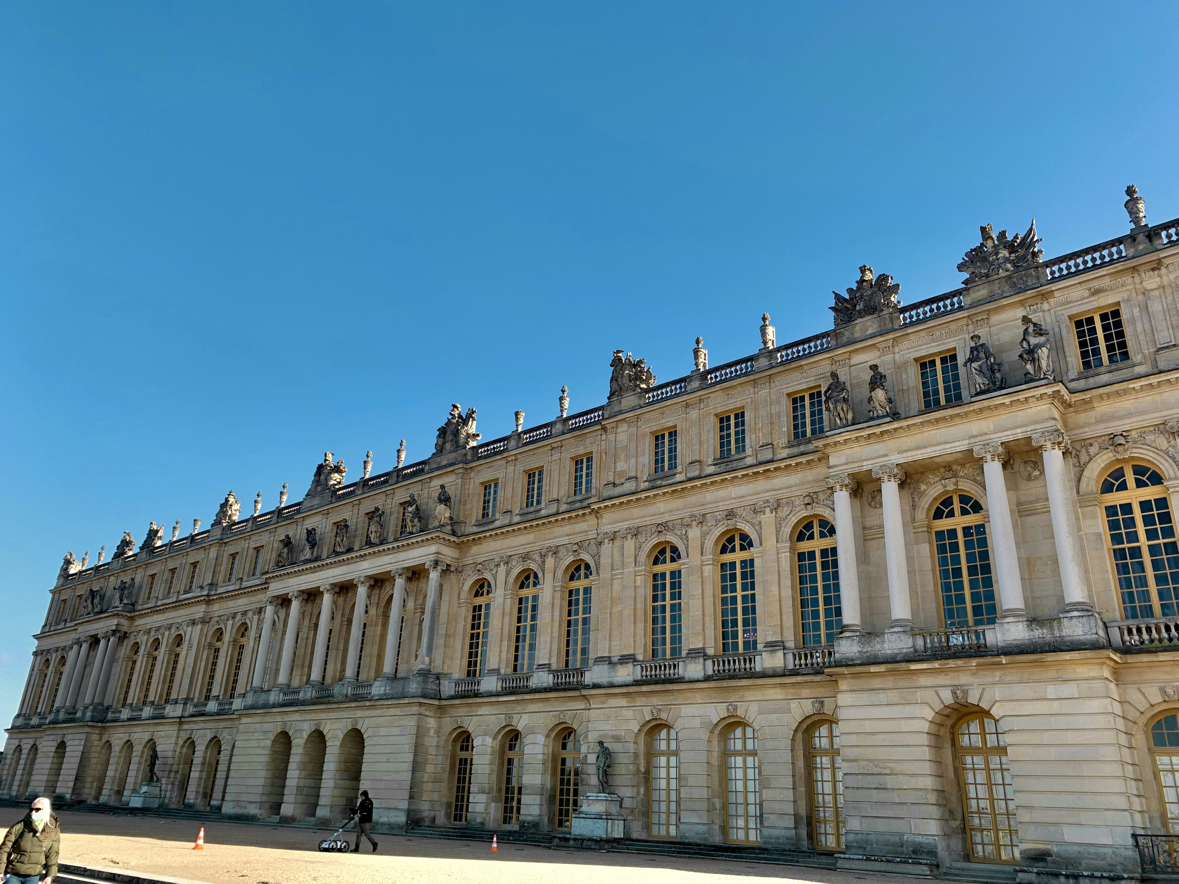 Imposing facade of the Palace of Versailles showcasing intricate architectural details and grand windows under a clear blue sky.