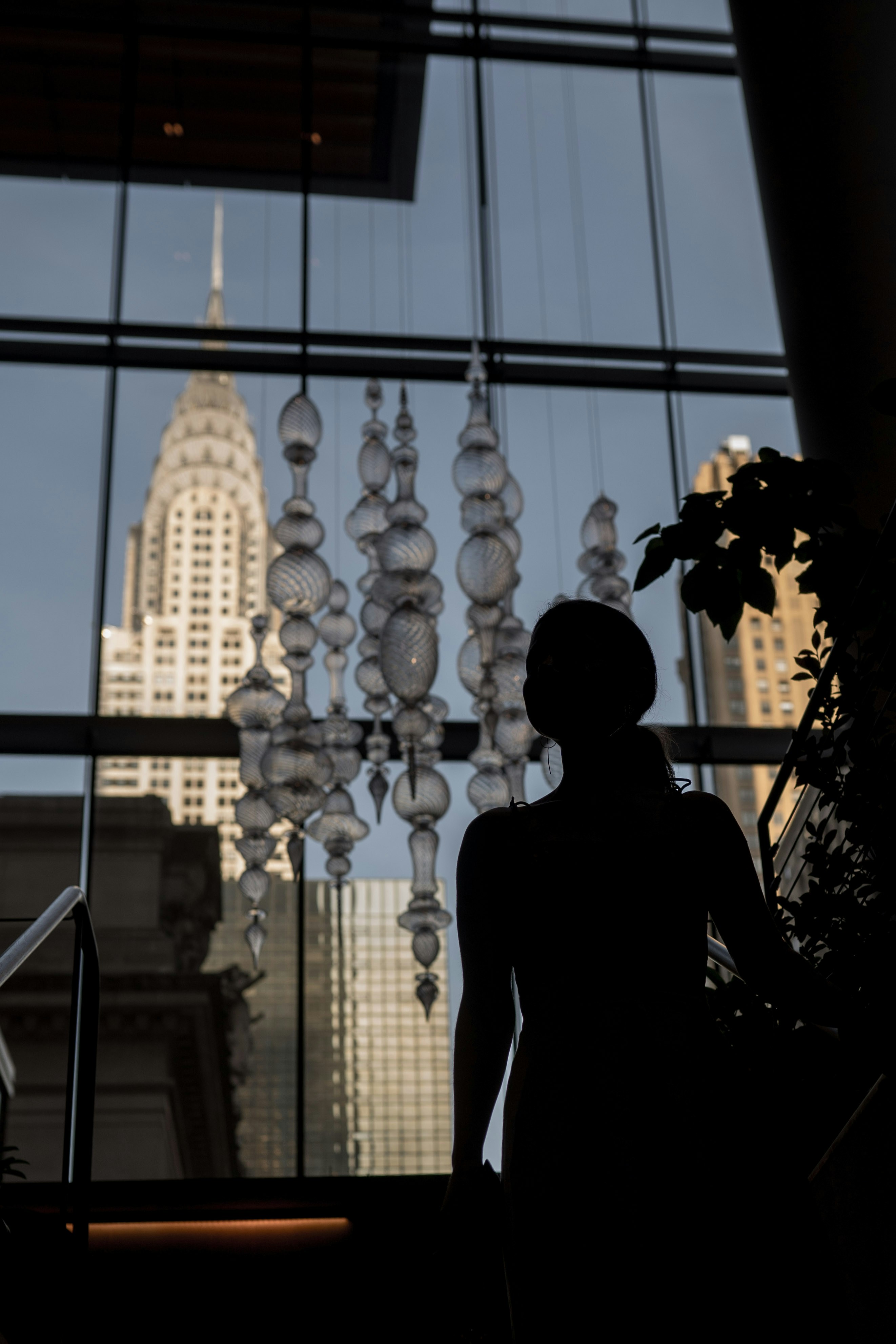 Silhouette against urban glass: a quiet figure dwarfed by crystalline mobiles
