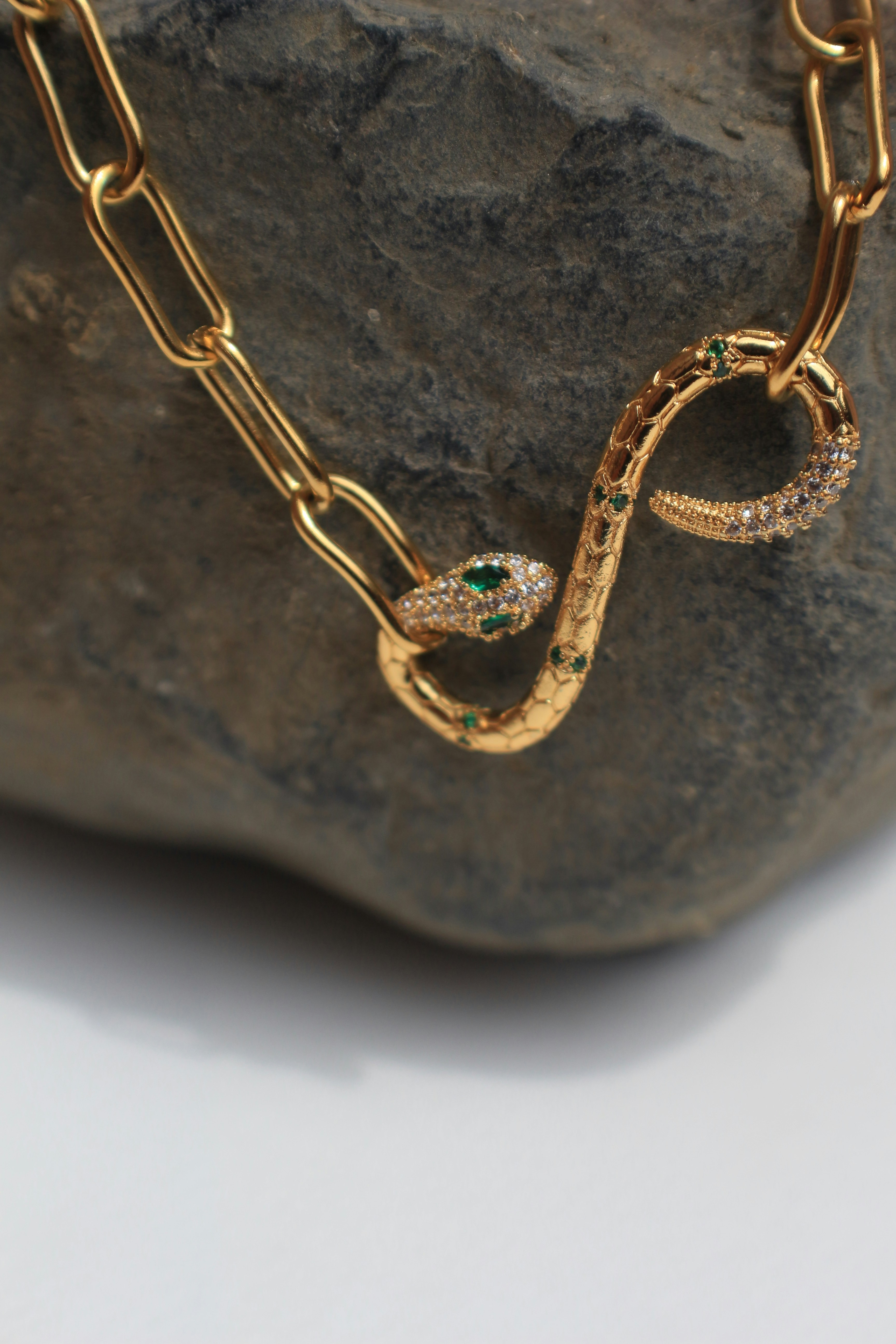 Coiled gold serpent necklace resting on a rugged rock