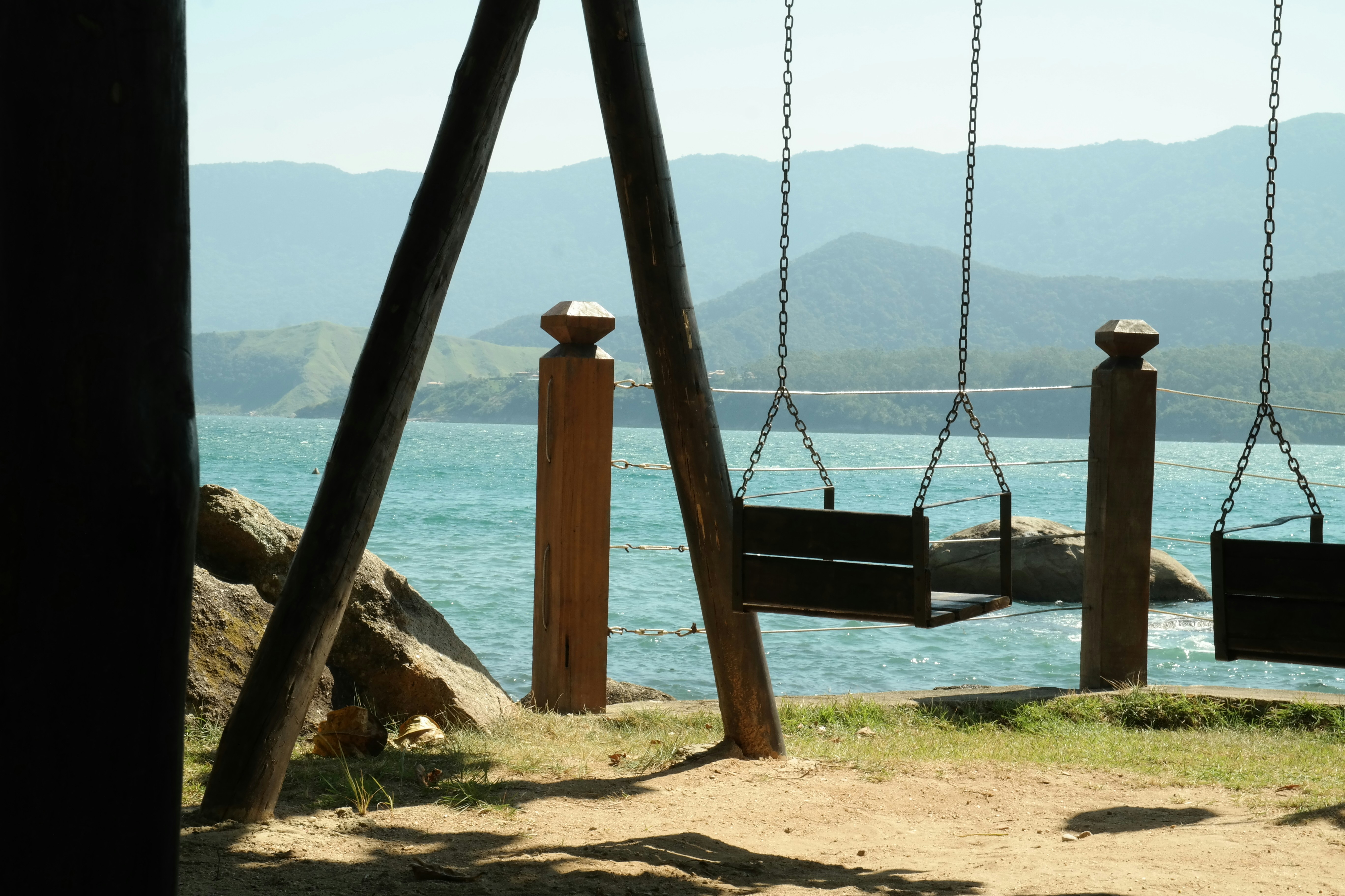 Wooden swing set overlooking a serene body of water with distant mountains under a clear sky.