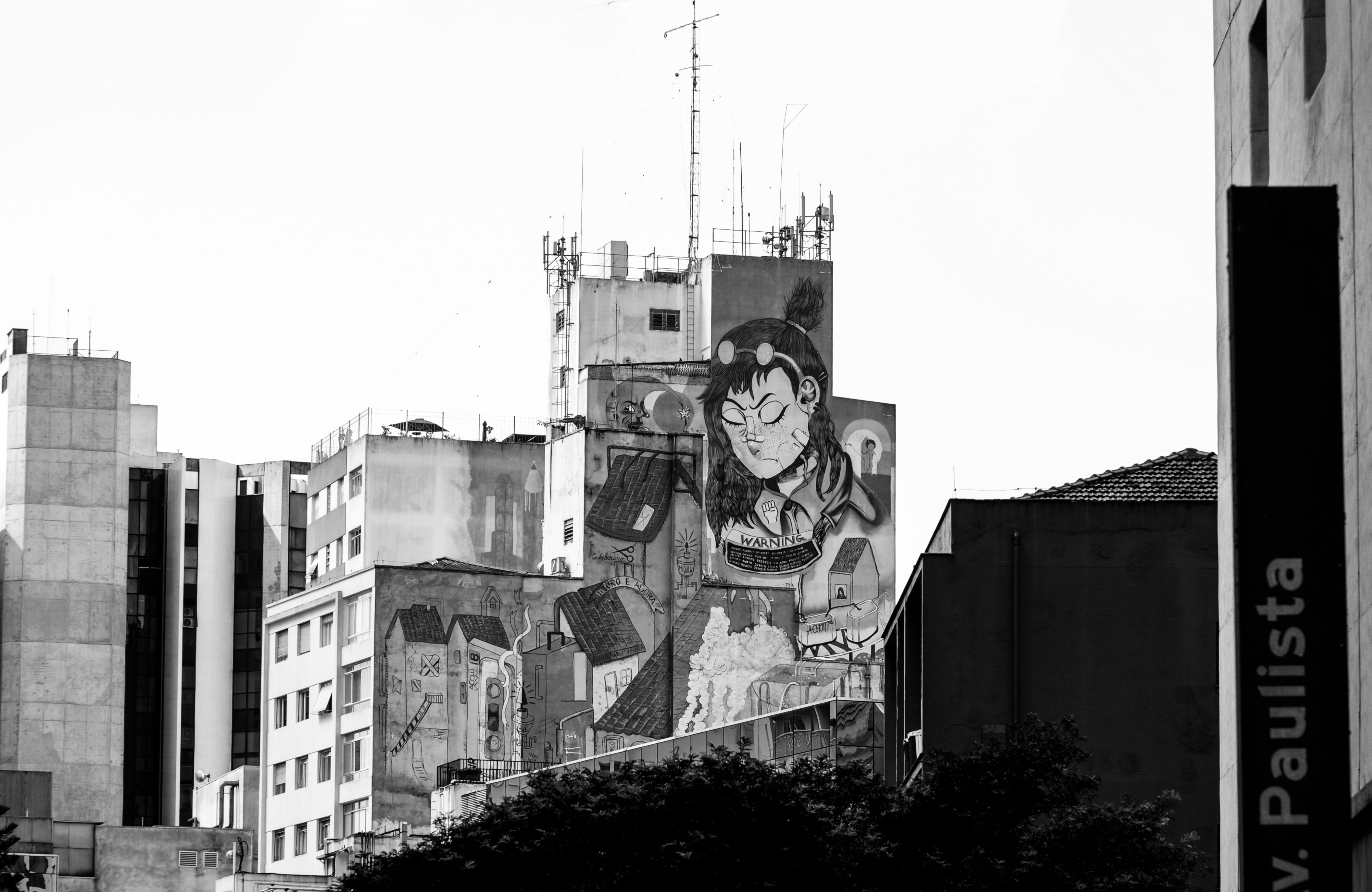 Colorful murals adorn tall buildings under a bright sky on Avenida Paulista.