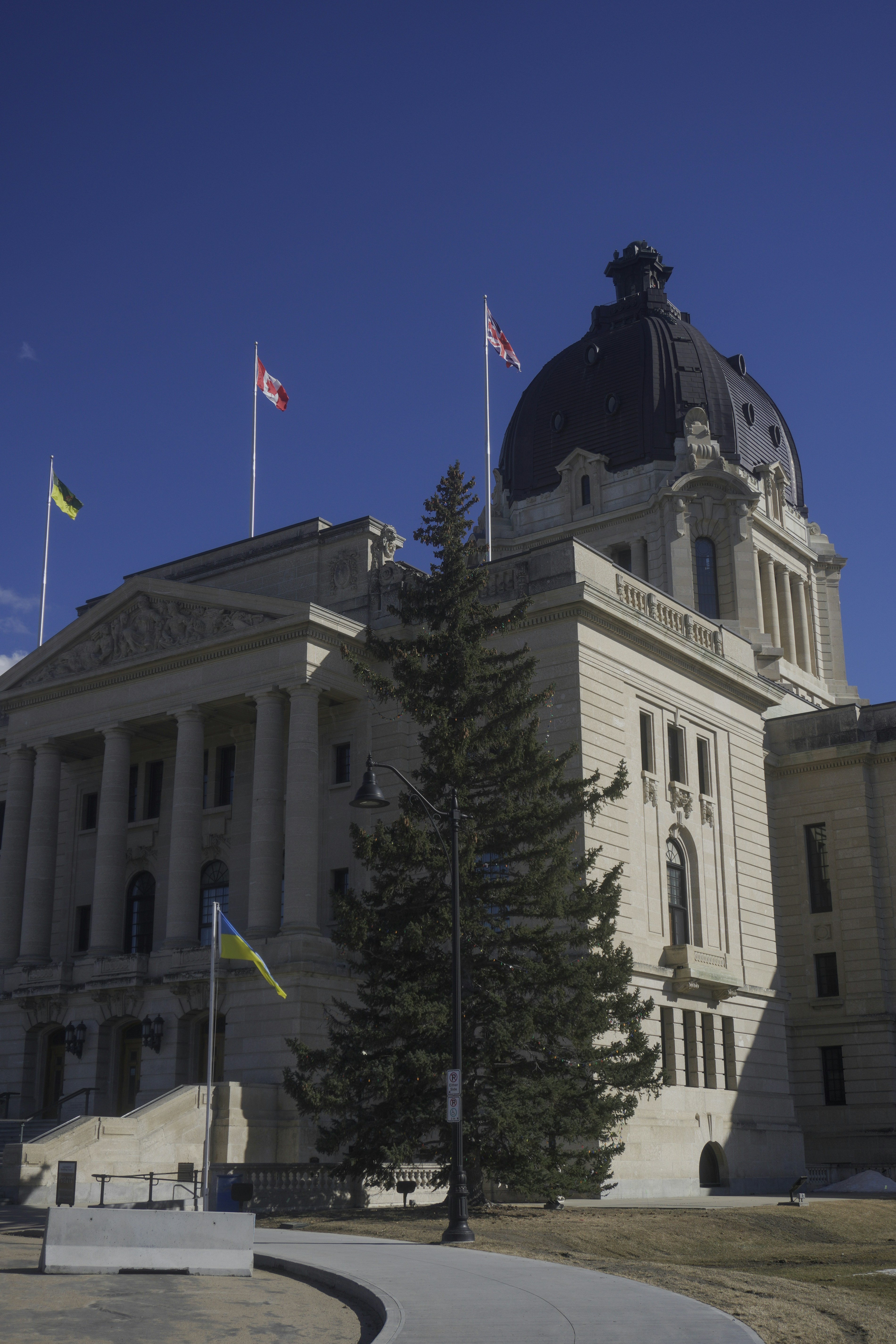 Historic building with a grand dome and multiple flags under a clear blue sky.
