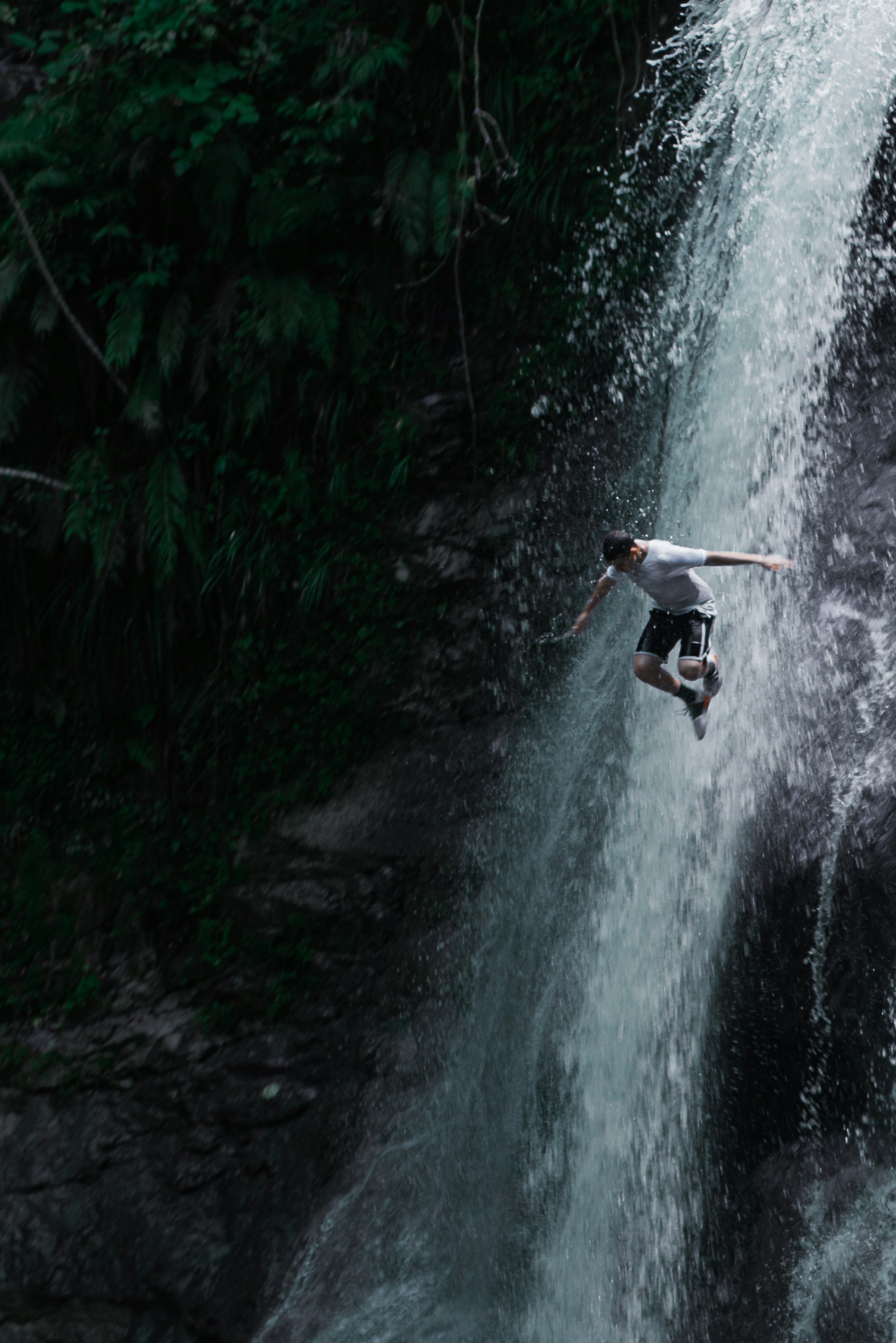 Adventurer diving off a waterfall surrounded by lush greenery, capturing the thrill of nature's playground.