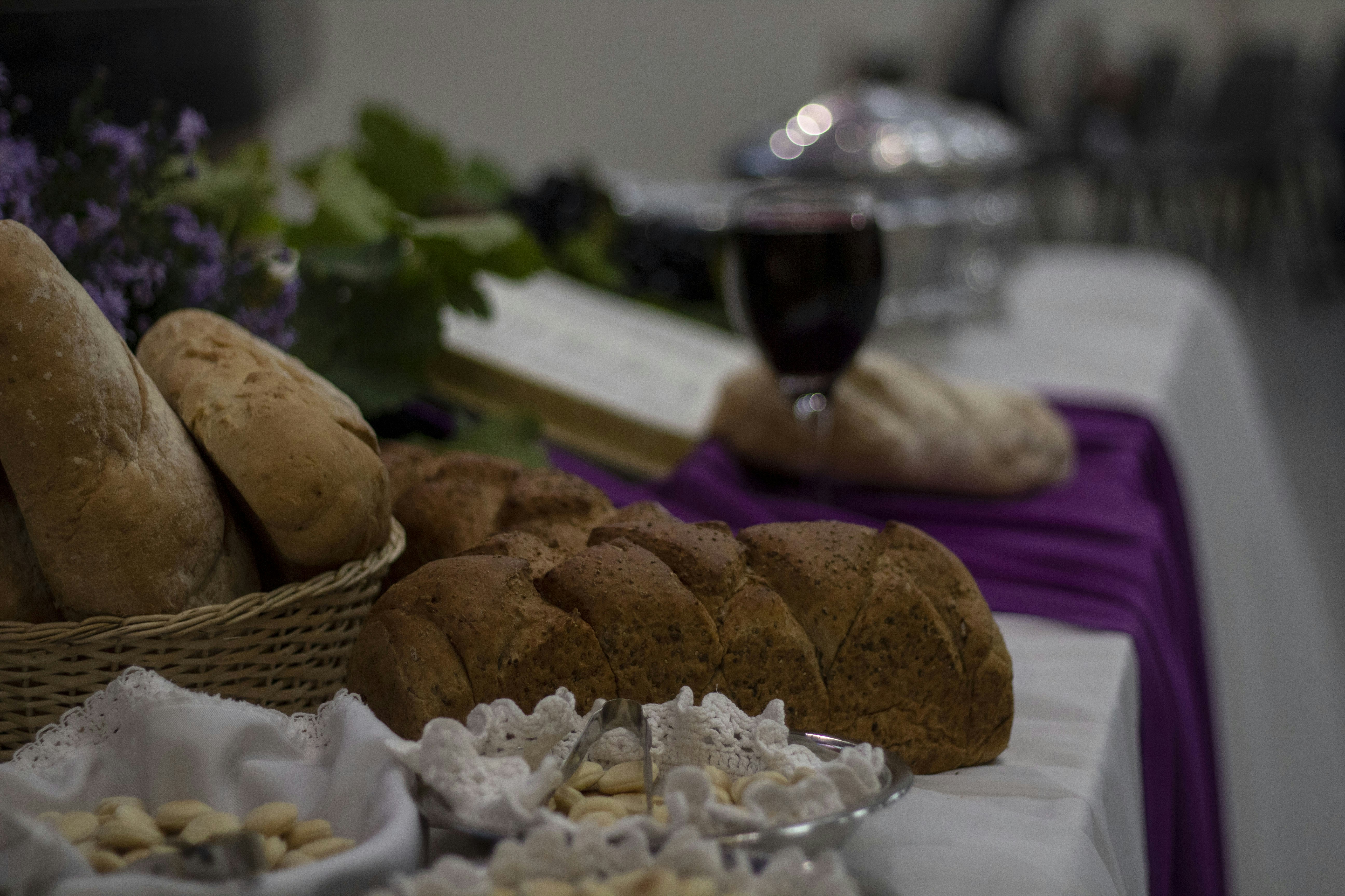 A beautifully arranged table featuring various breads, a glass of wine, and decorative elements like grapes and flowers, symbolizing community and celebration.