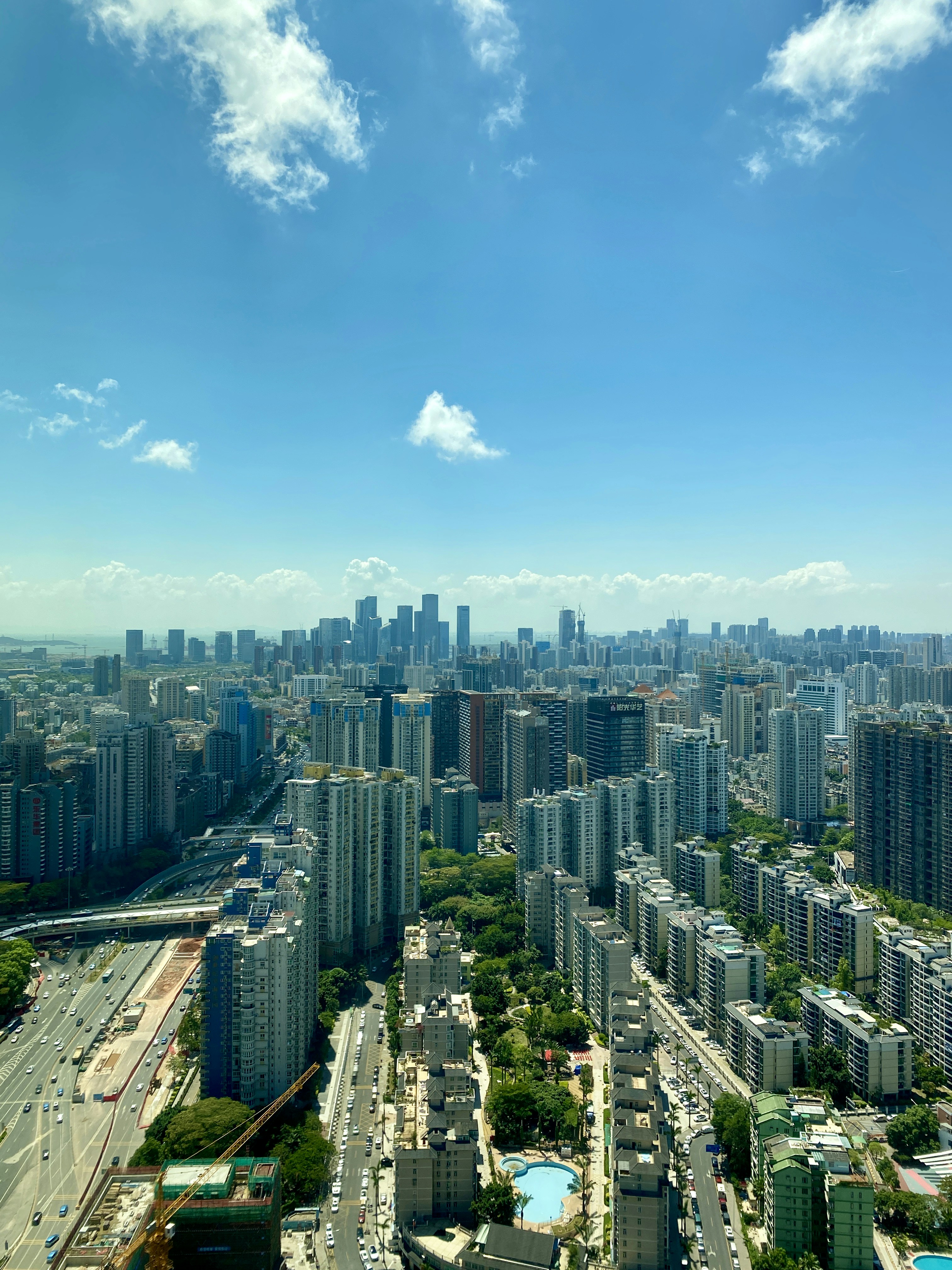 A panoramic view of a bustling cityscape featuring high-rise buildings and busy highways under a clear blue sky.