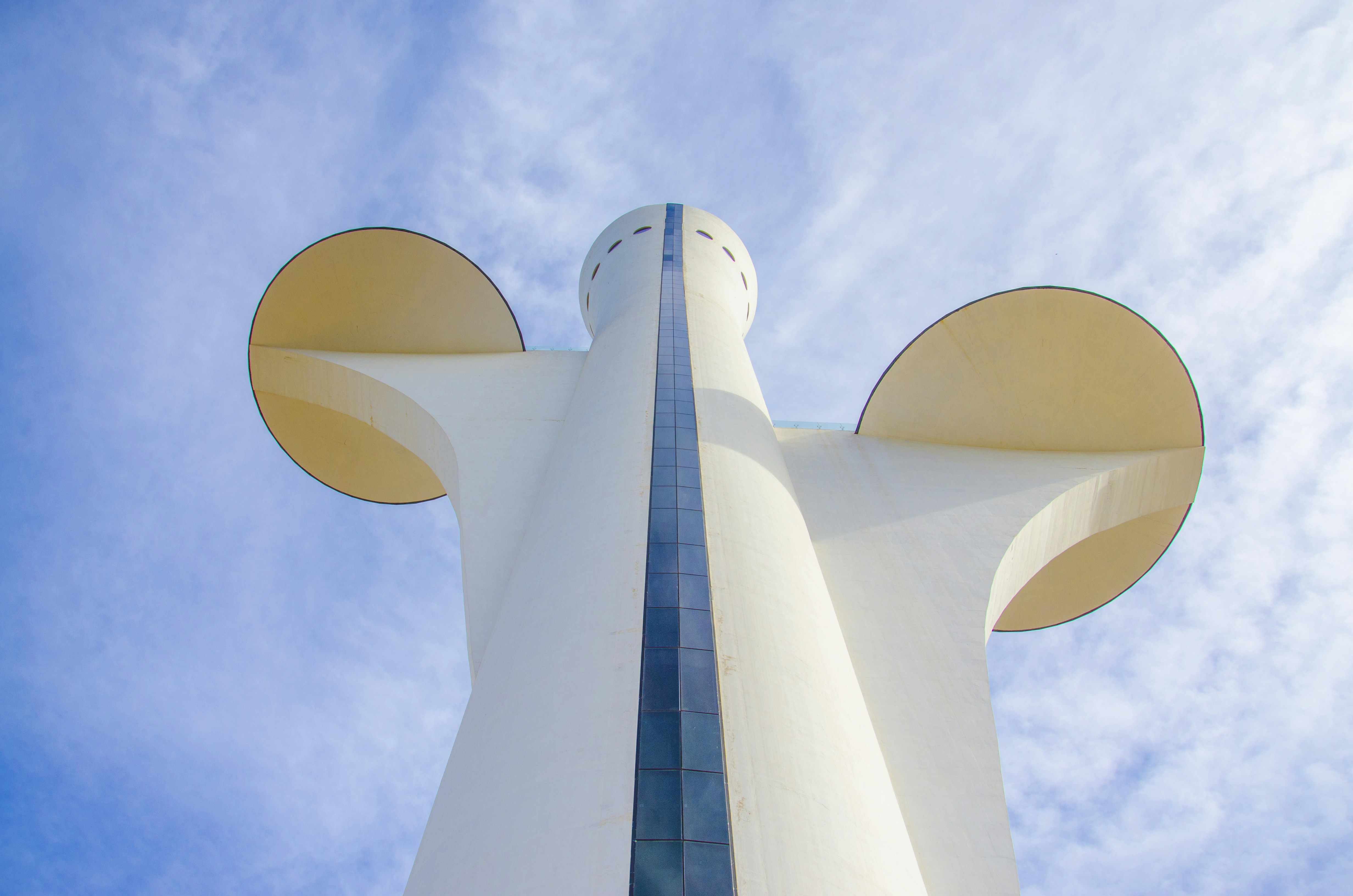 Sleek white tower with circular extensions reaching into a blue sky.