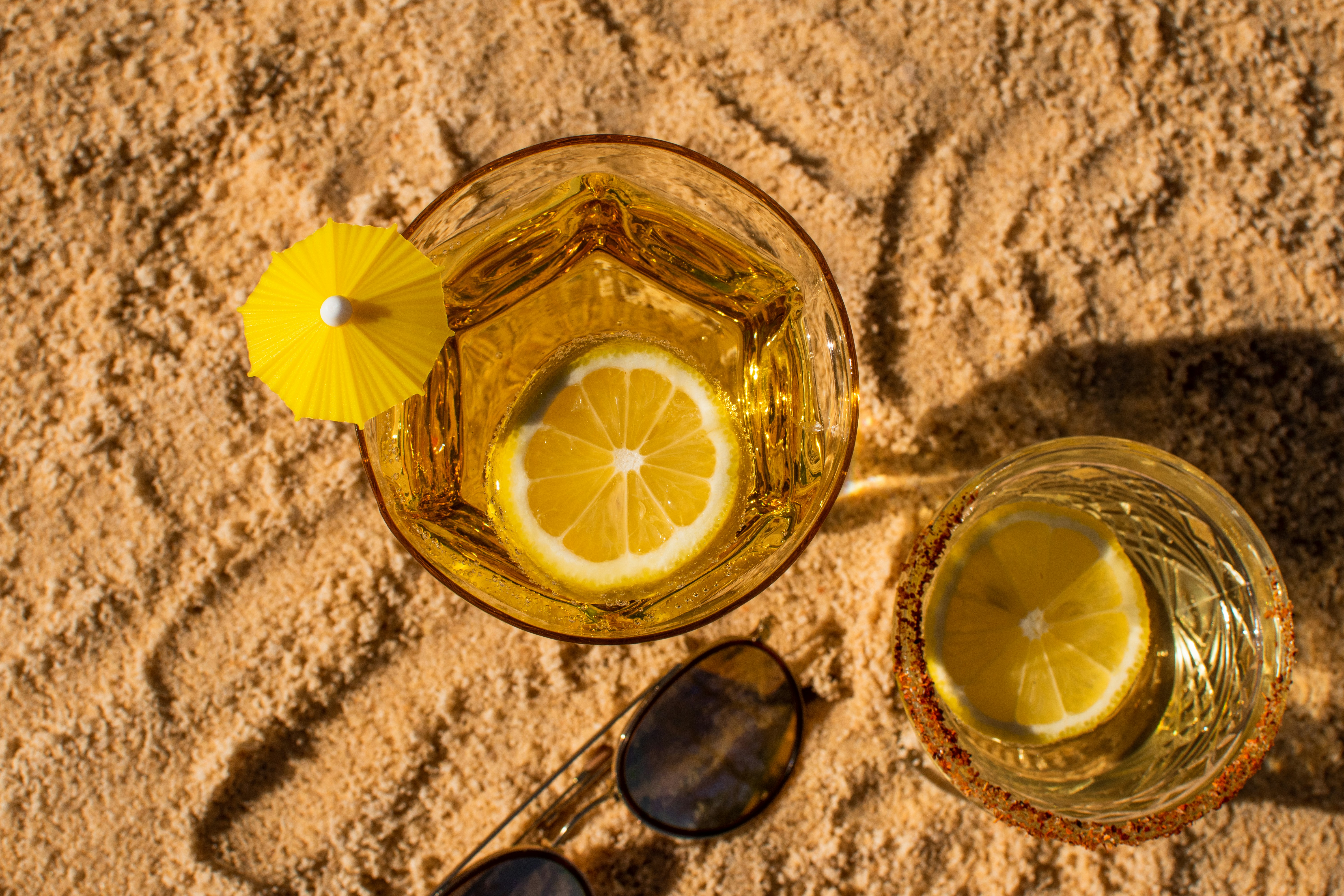 Yellow drink and sunglasses on beach sand in hard light