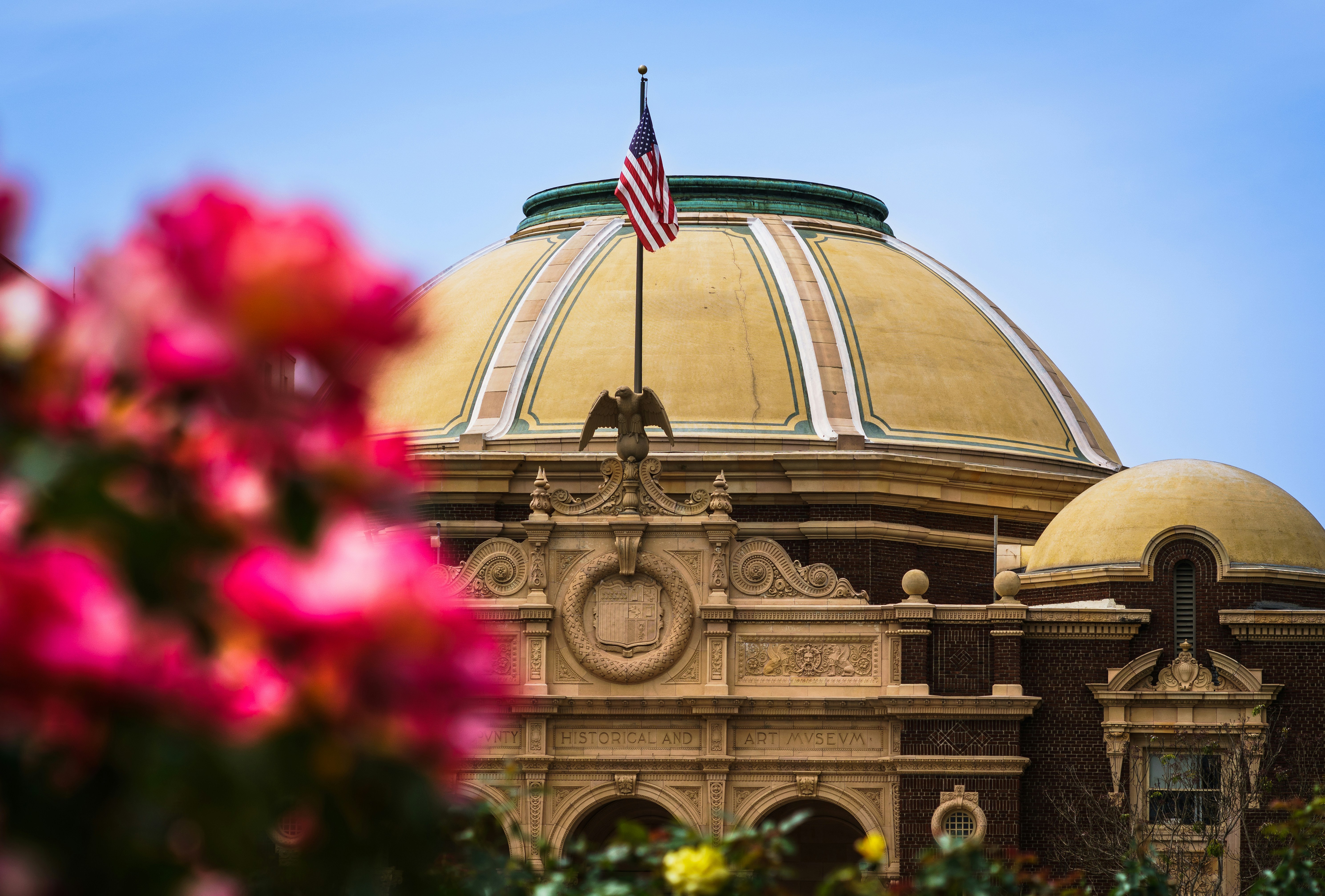 Flag atop Beaux-Arts Dome, framed by pink blooms and a cobalt sky