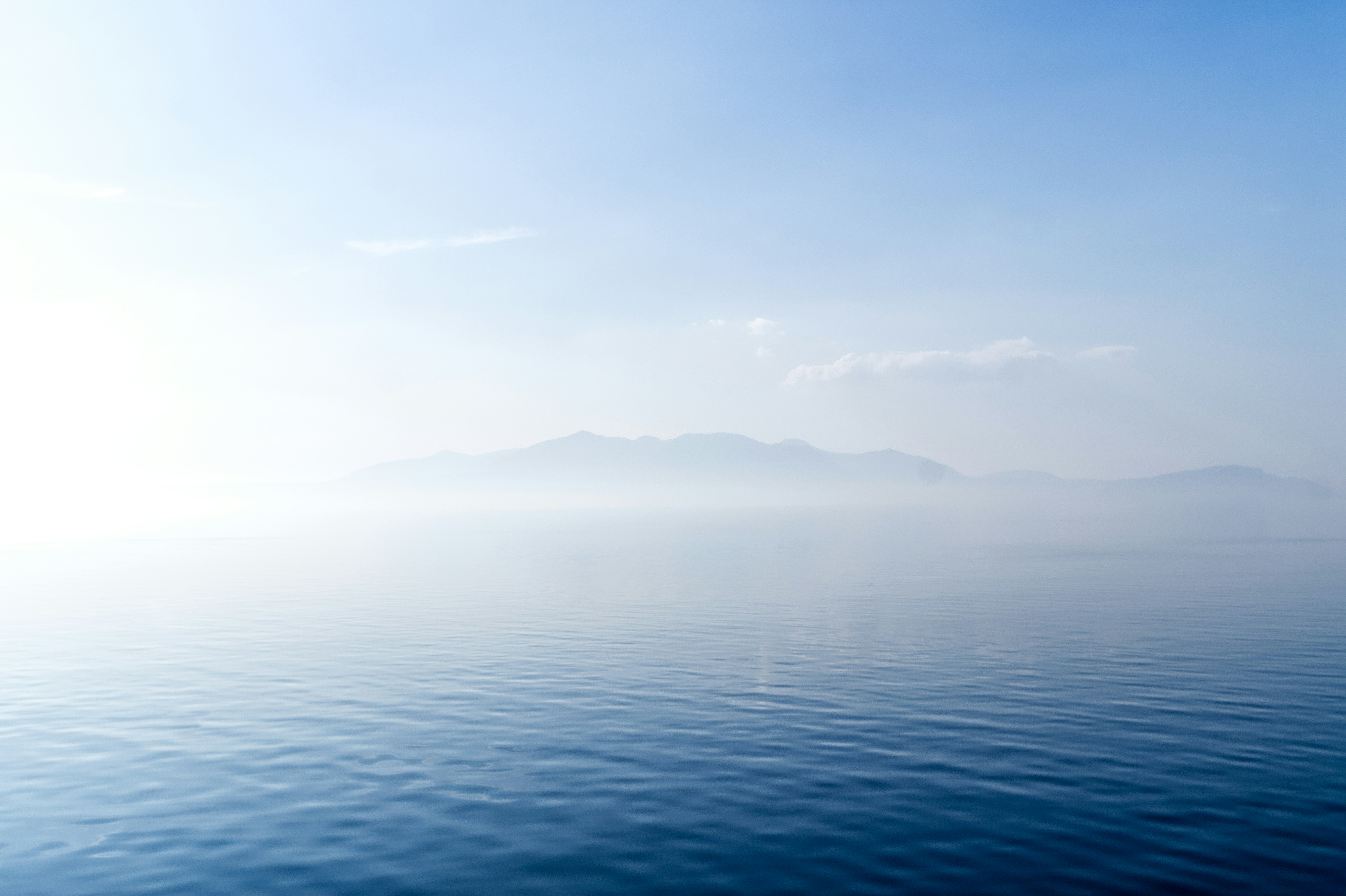 Distant silhouette of the Isle of Arran enveloped in mist over calm blue waters under a clear sky.